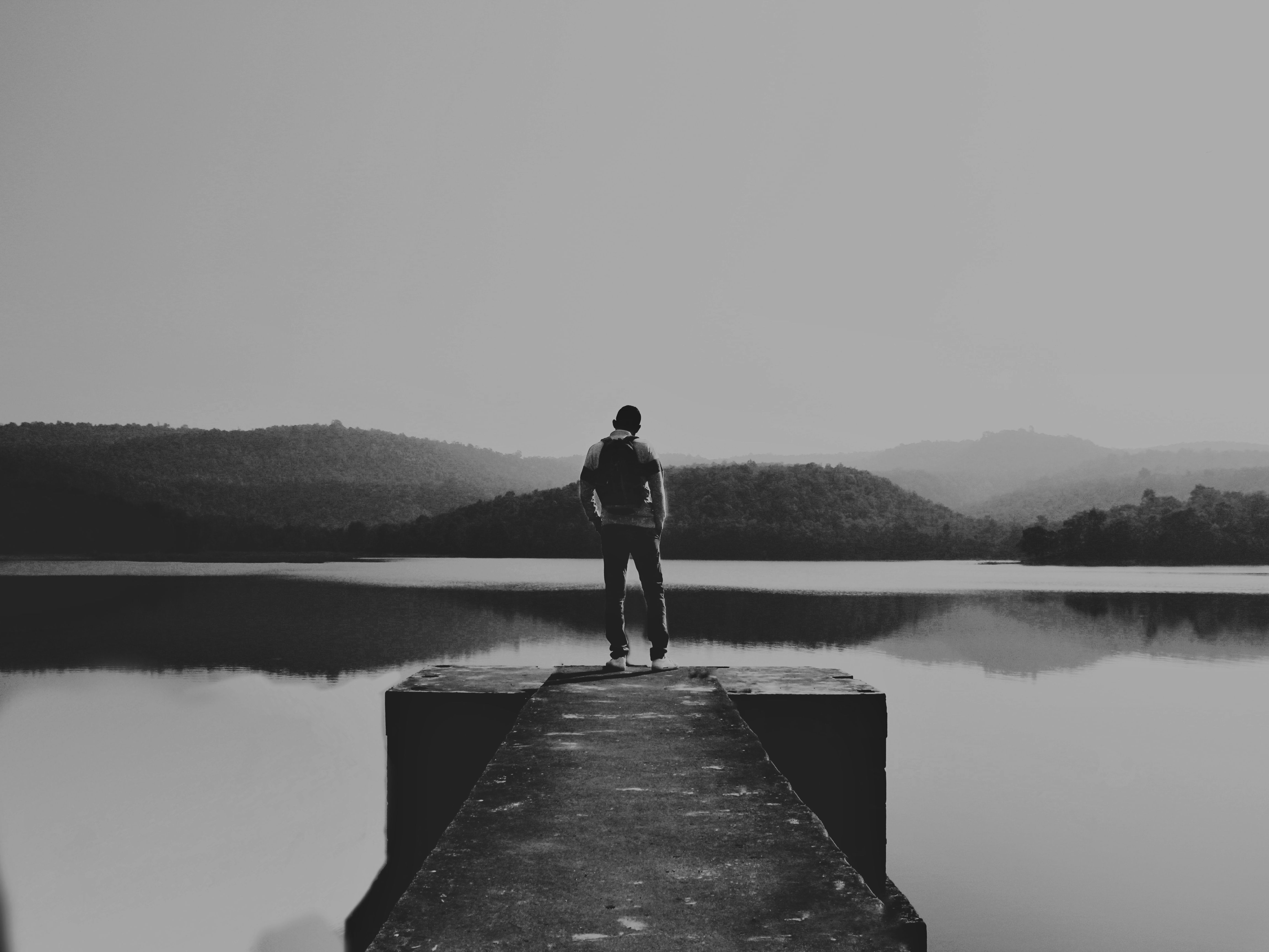 Grayscale Photo of a Man Walking on Wooden Dock Waving · Free Stock Photo
