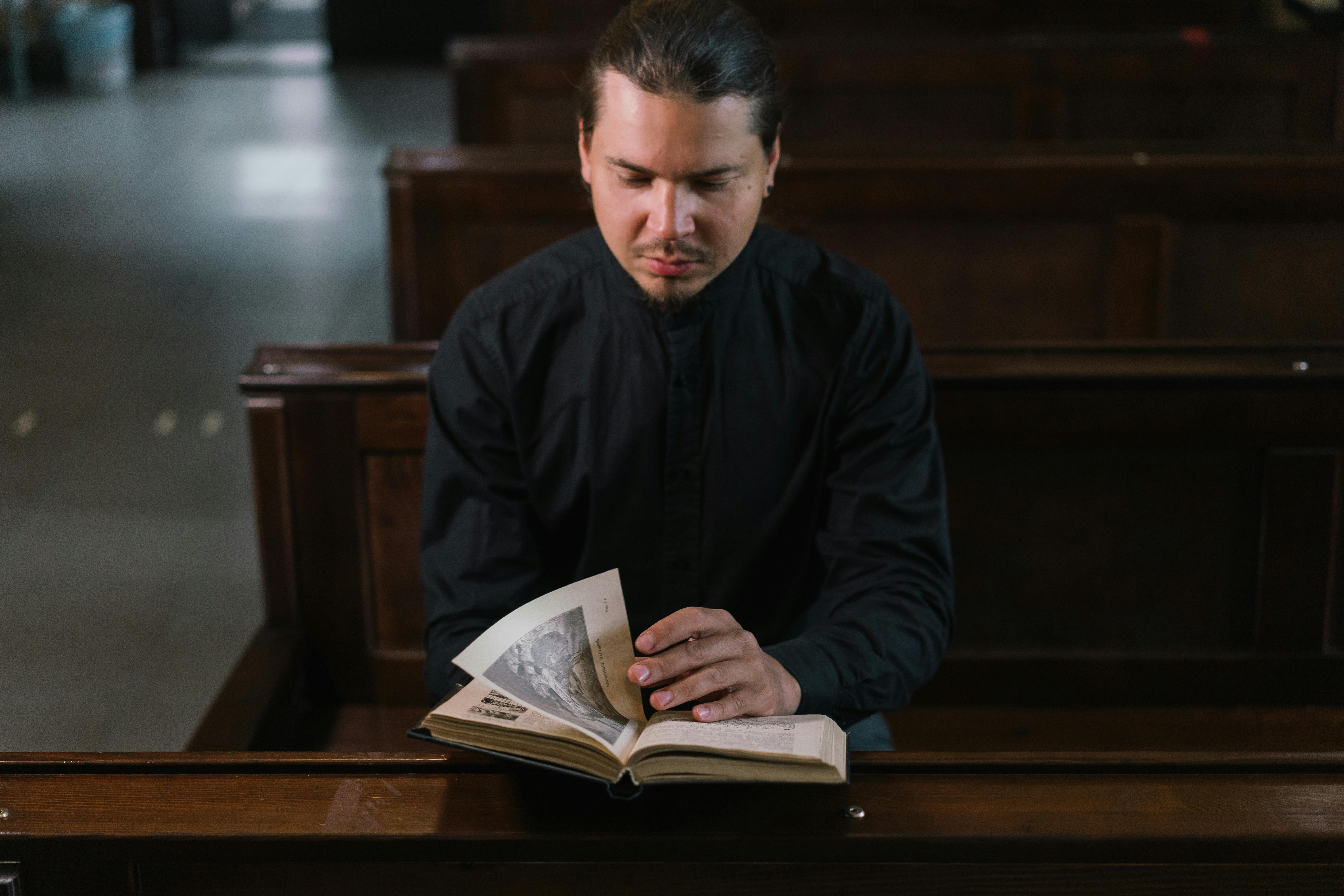 Man in Black Clothes Inside a Church Reading a Bible · Free Stock Photo