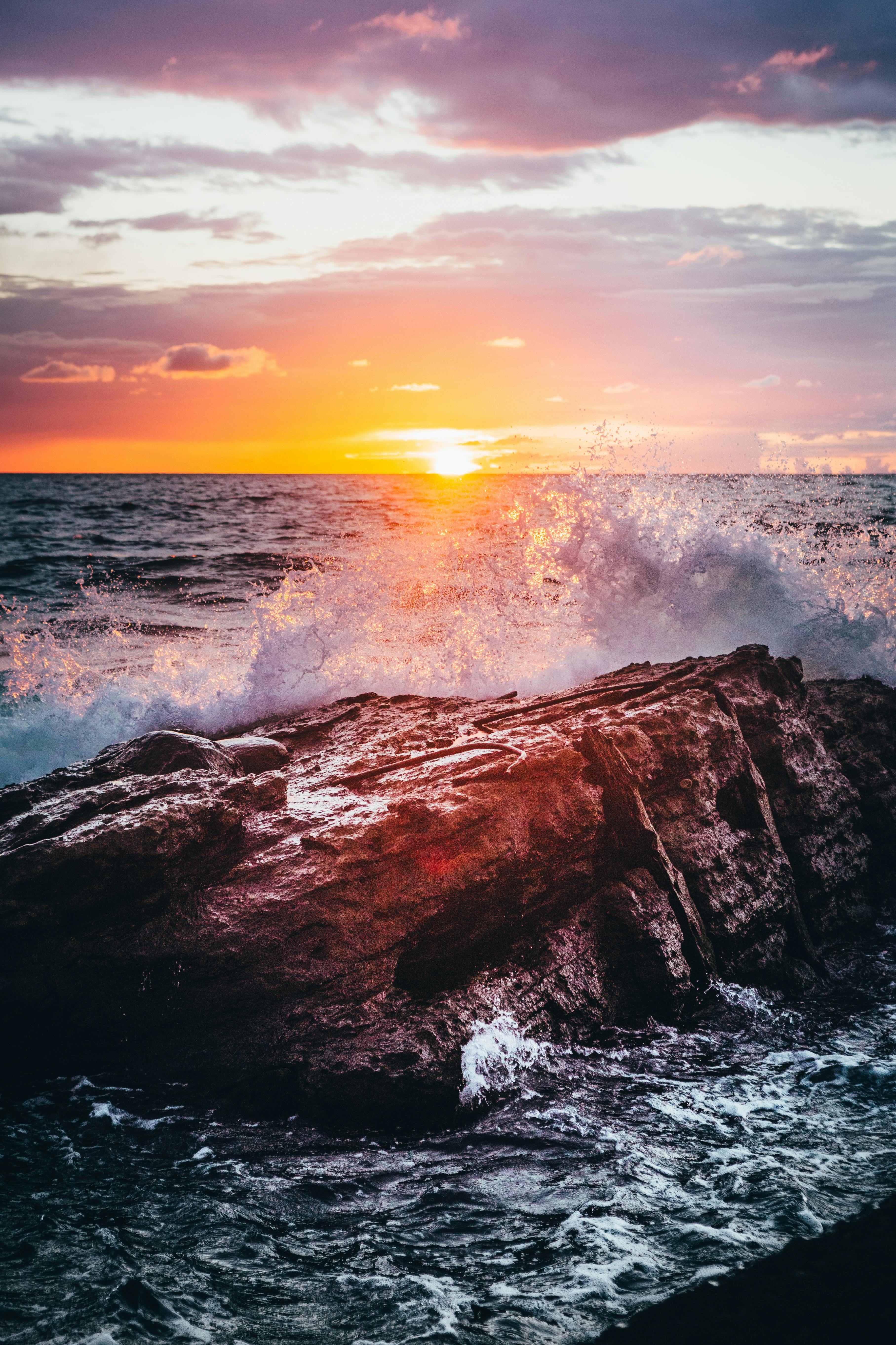 A Dramatic Sunset Over the Sea with Splashing Waves on a Rock Formation ...