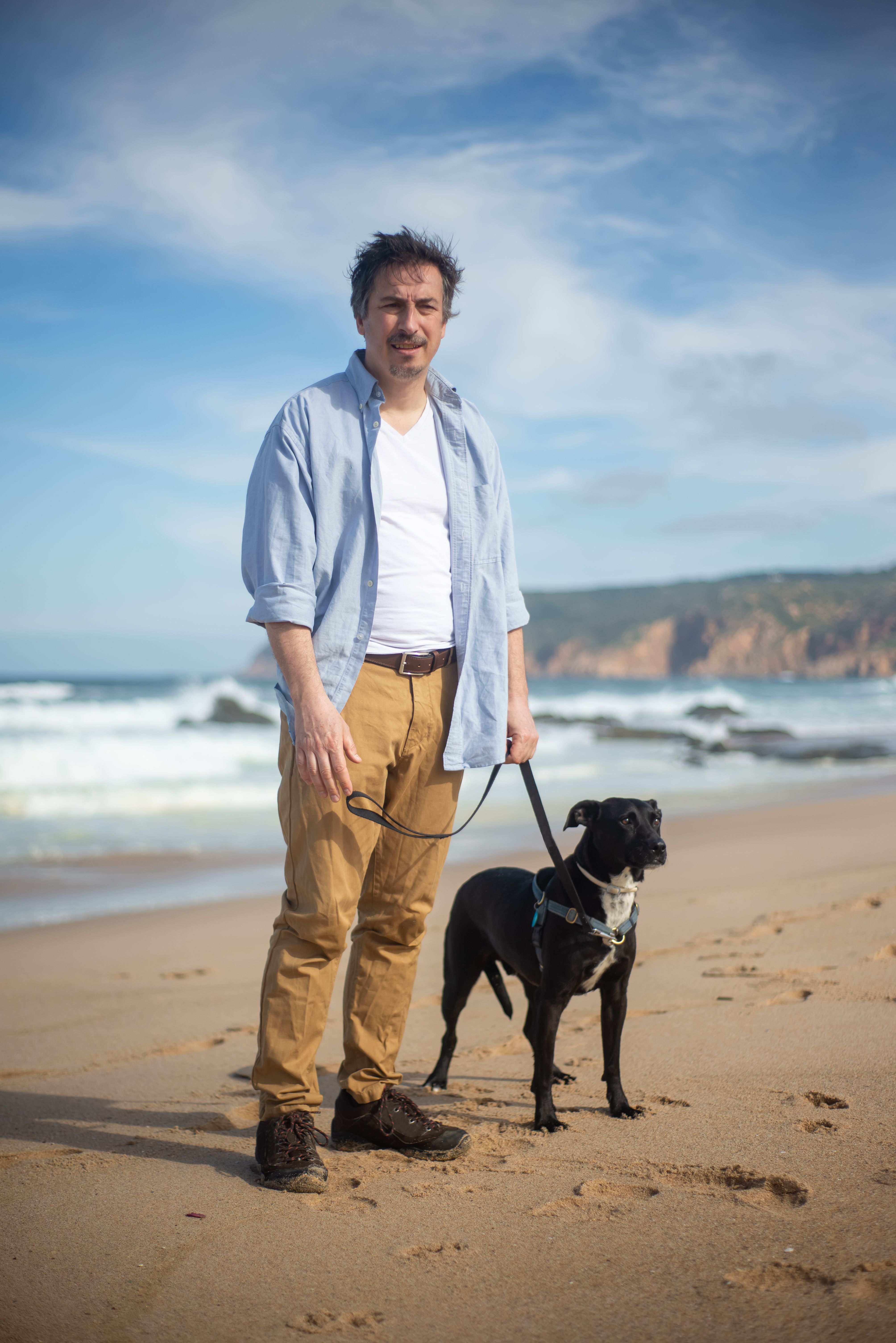 A Man in Blue Polo Shirt Standing on Sand with a Black Short Coated Dog ...