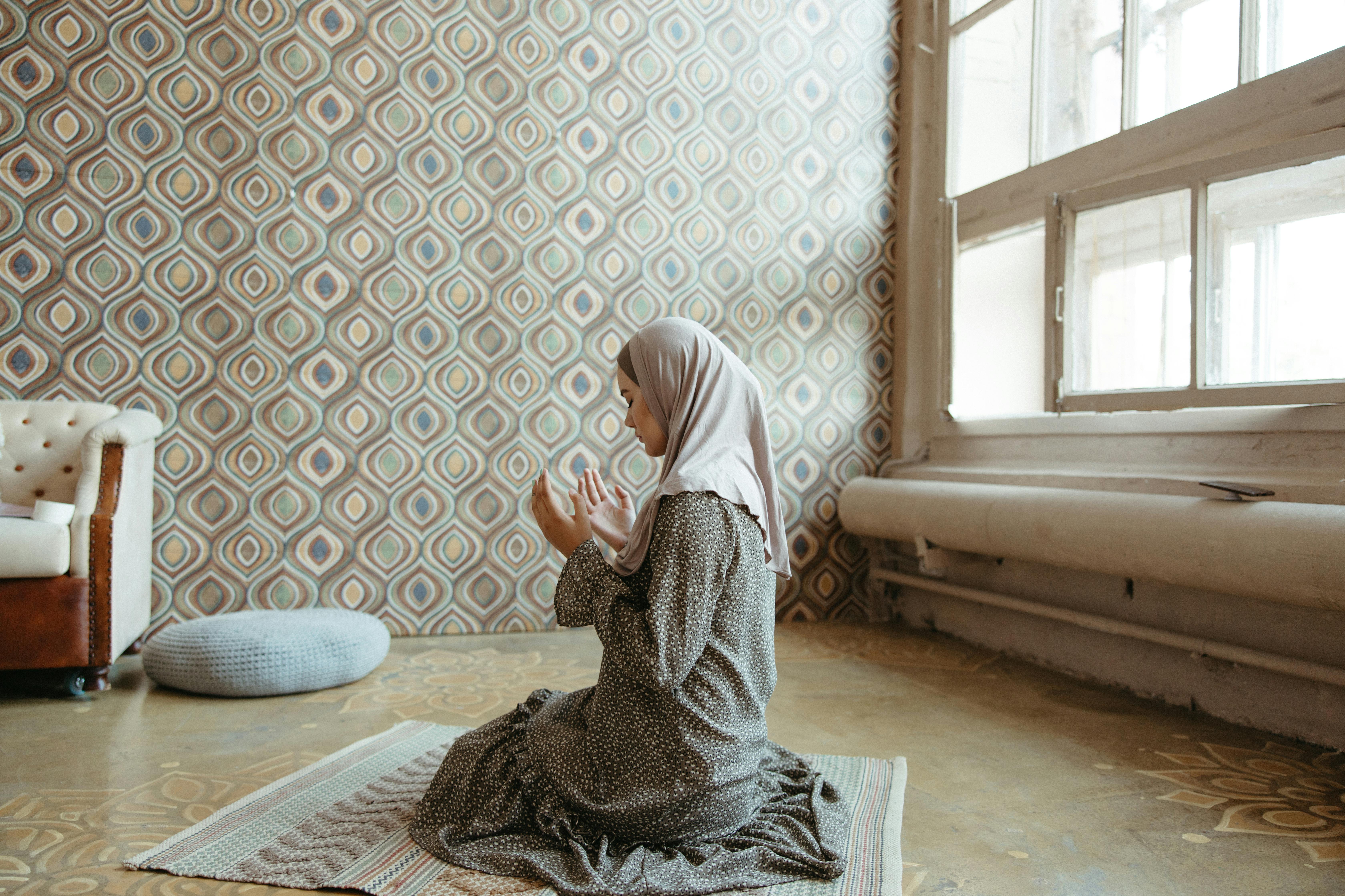 Woman in Long Dress and Headscarf Praying on a Rug · Free Stock Photo
