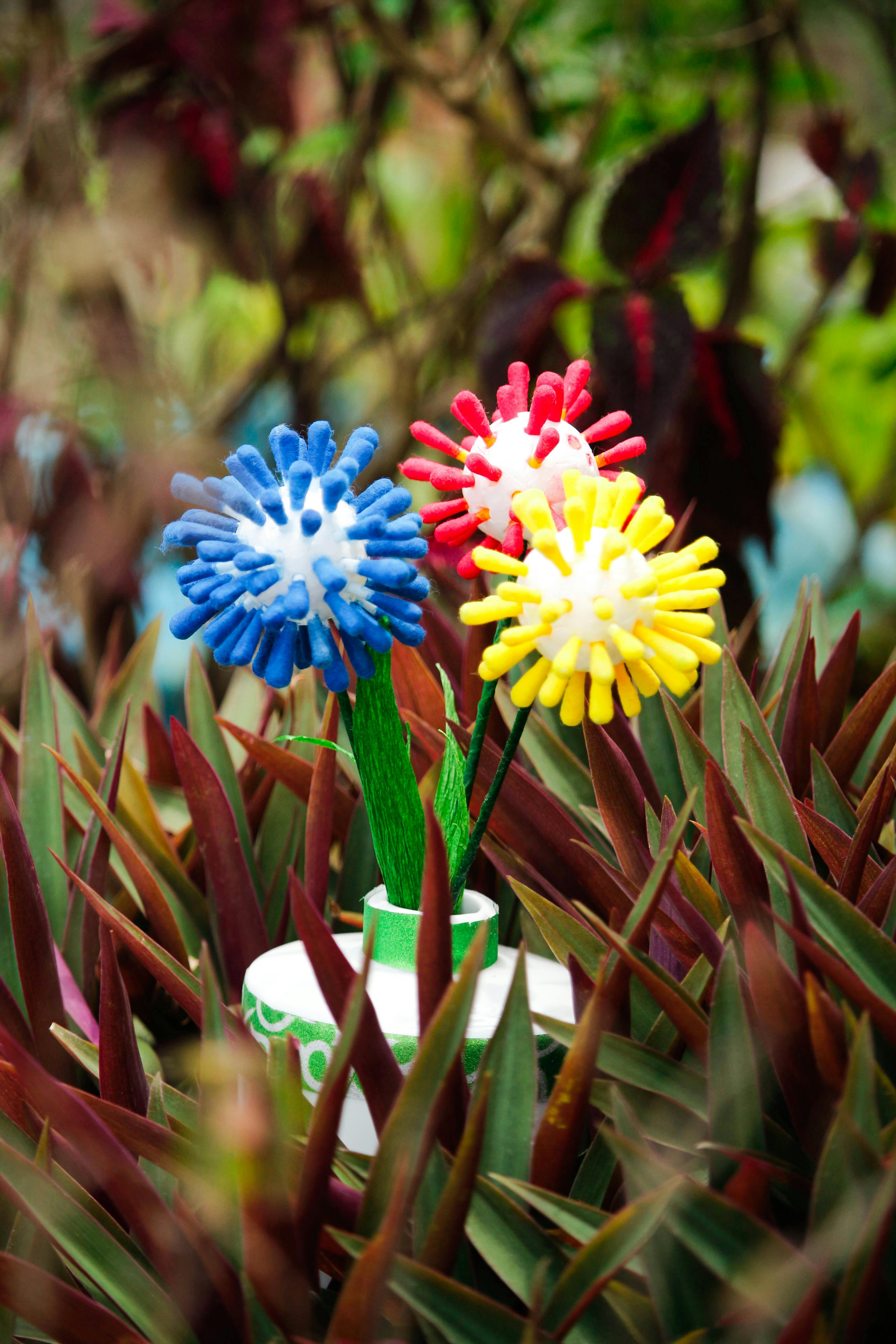 Vase with Bright Fake Flowers Standing Among Real Plants · Free Stock Photo
