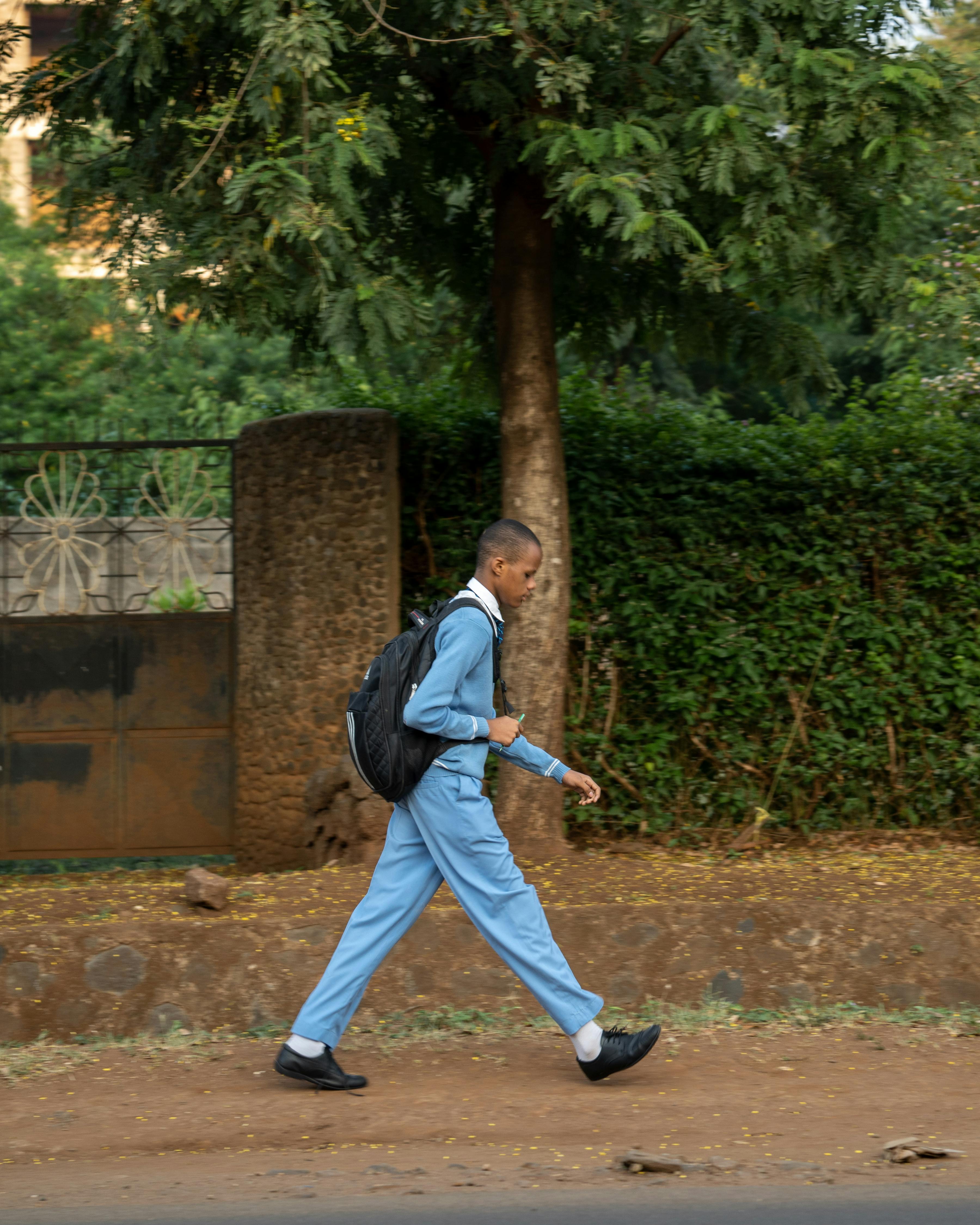 A Student Carrying a Backpack Walking on a Sidewalk · Free Stock Photo