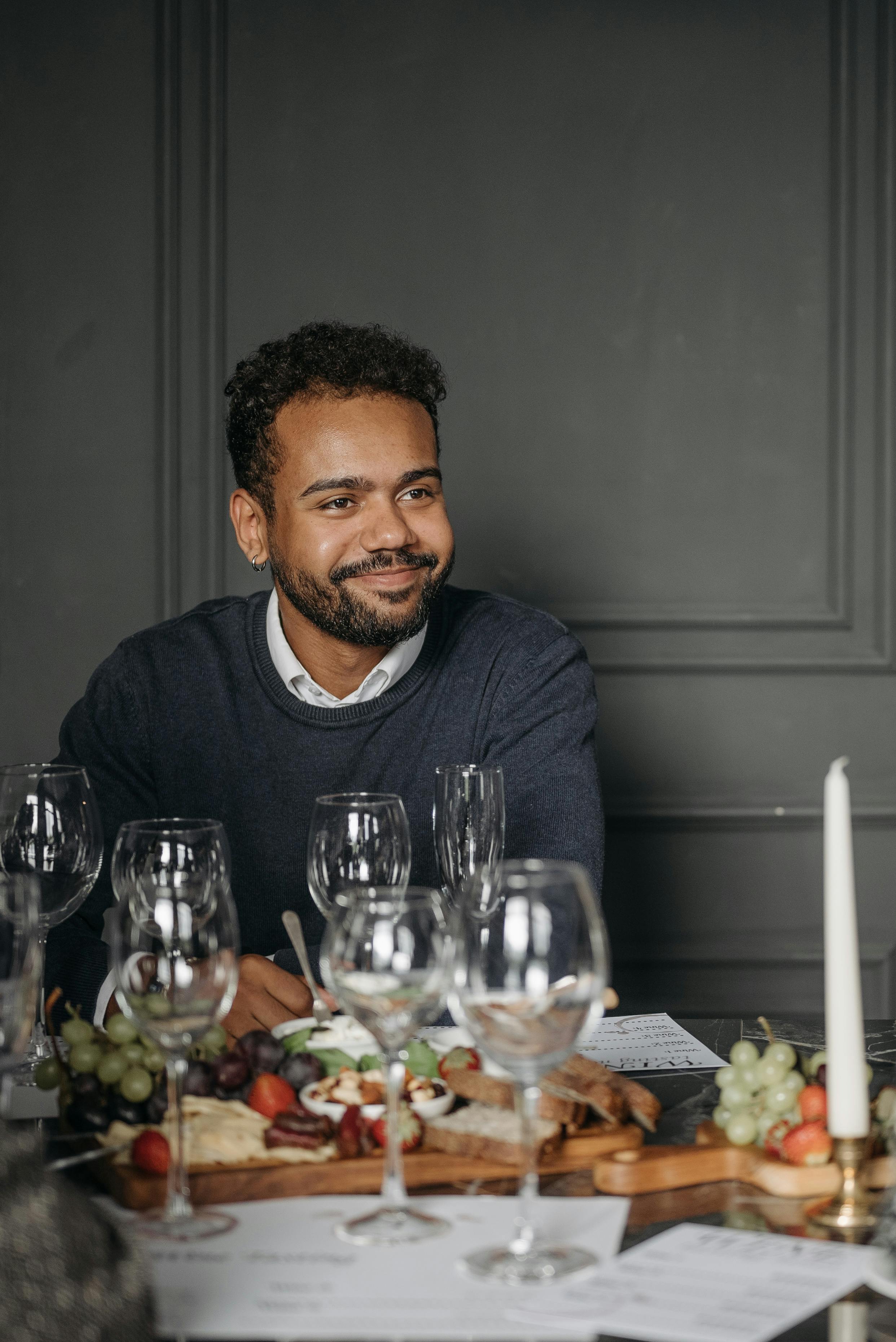 Man in Gray Sweatrer sitting beside a Table Full of Wine Glasses · Free ...