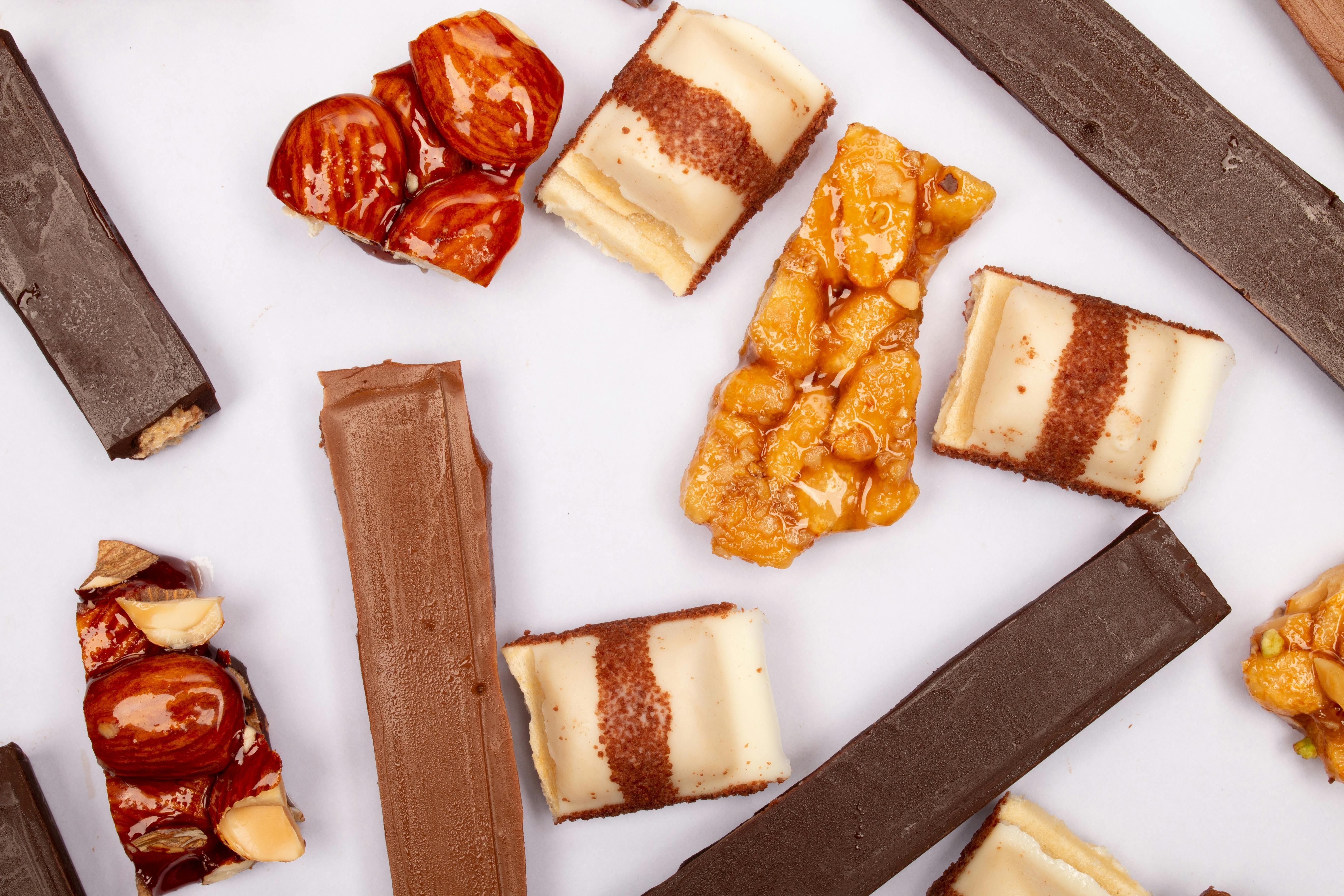 Assorted Chocolate Bars and Glazed Nuts on White Surface · Free Stock Photo