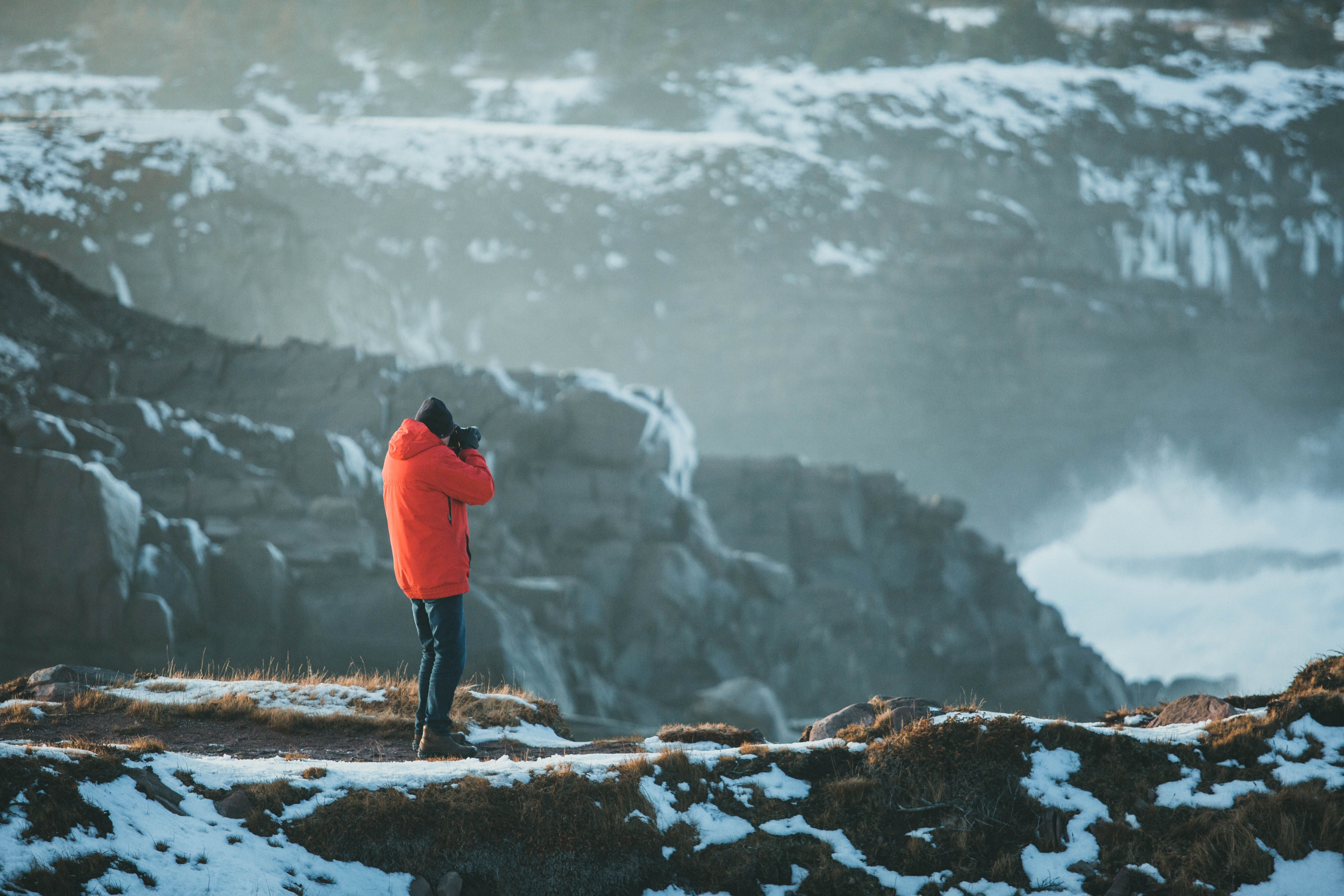 Person in Red Jacket Standing on Rock Mountain with Snow · Free Stock Photo