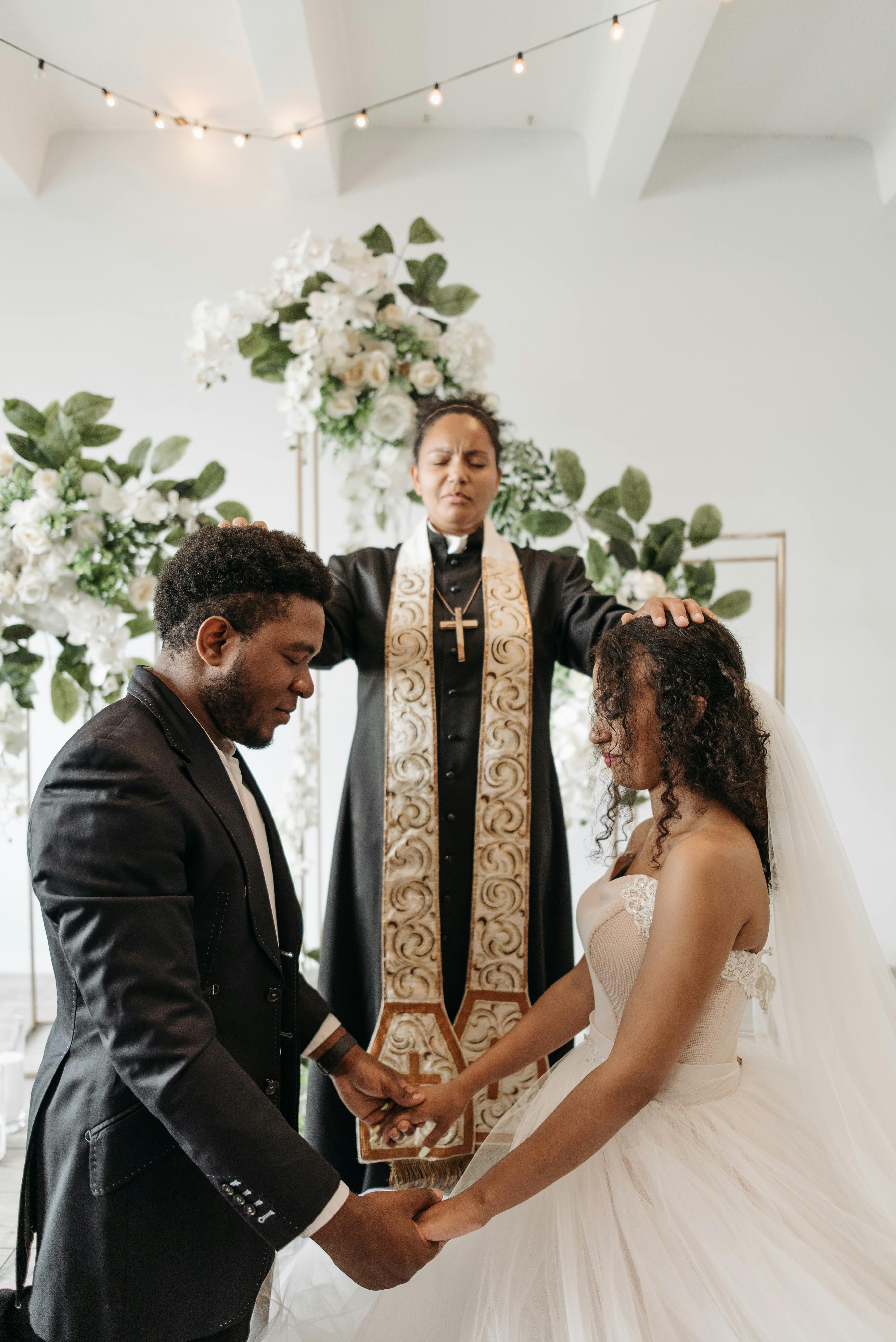 A Woman Pastor Touching the Heads of the Bride and Groom During a Pray ...