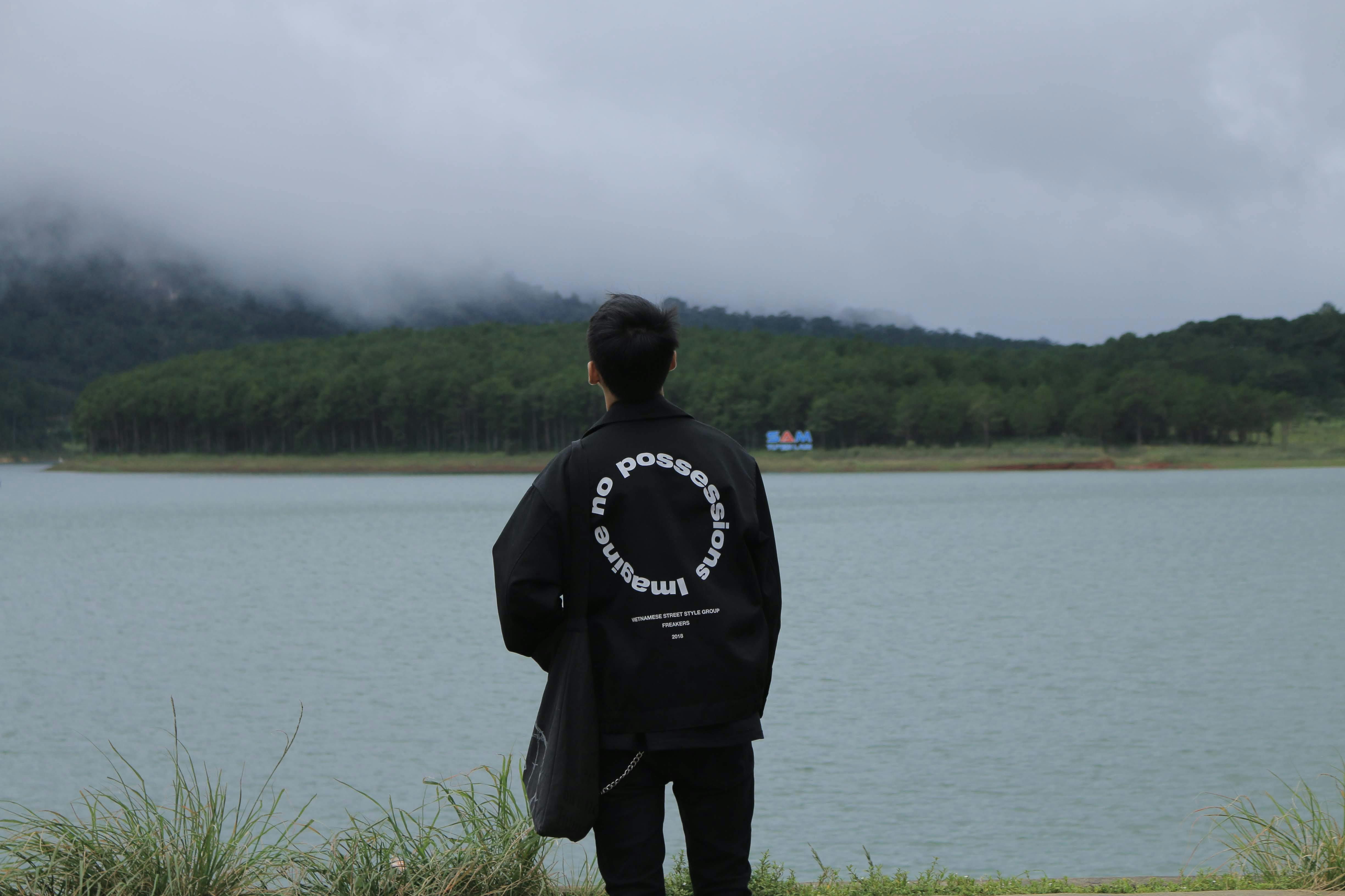 Back View of a Person Wearing a Black Jacket Standing Near a Lake ...