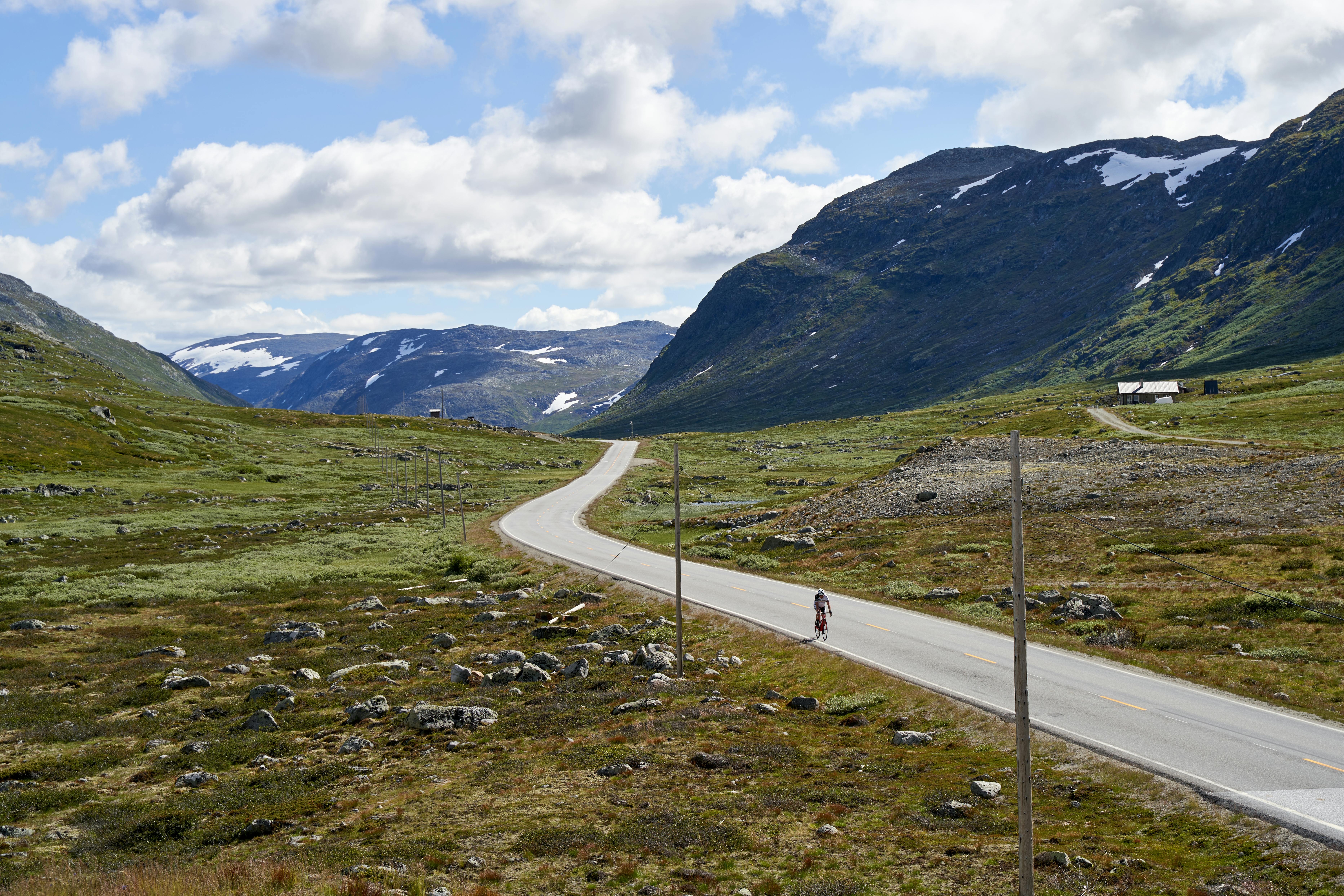 Person Cycling on a Road Between Mountains · Free Stock Photo