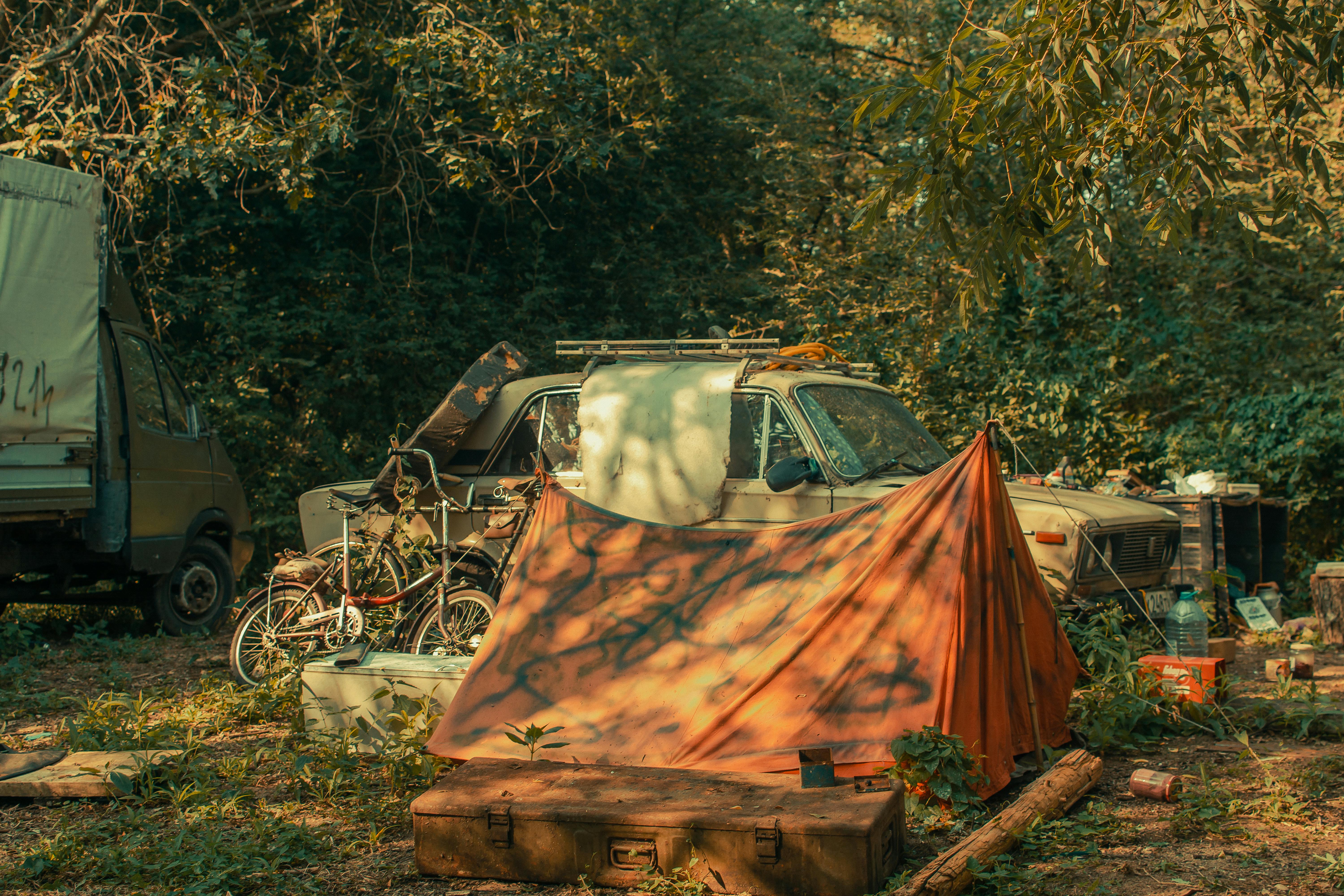 Vandalized Tent Set up in Junkyard among Trees · Free Stock Photo