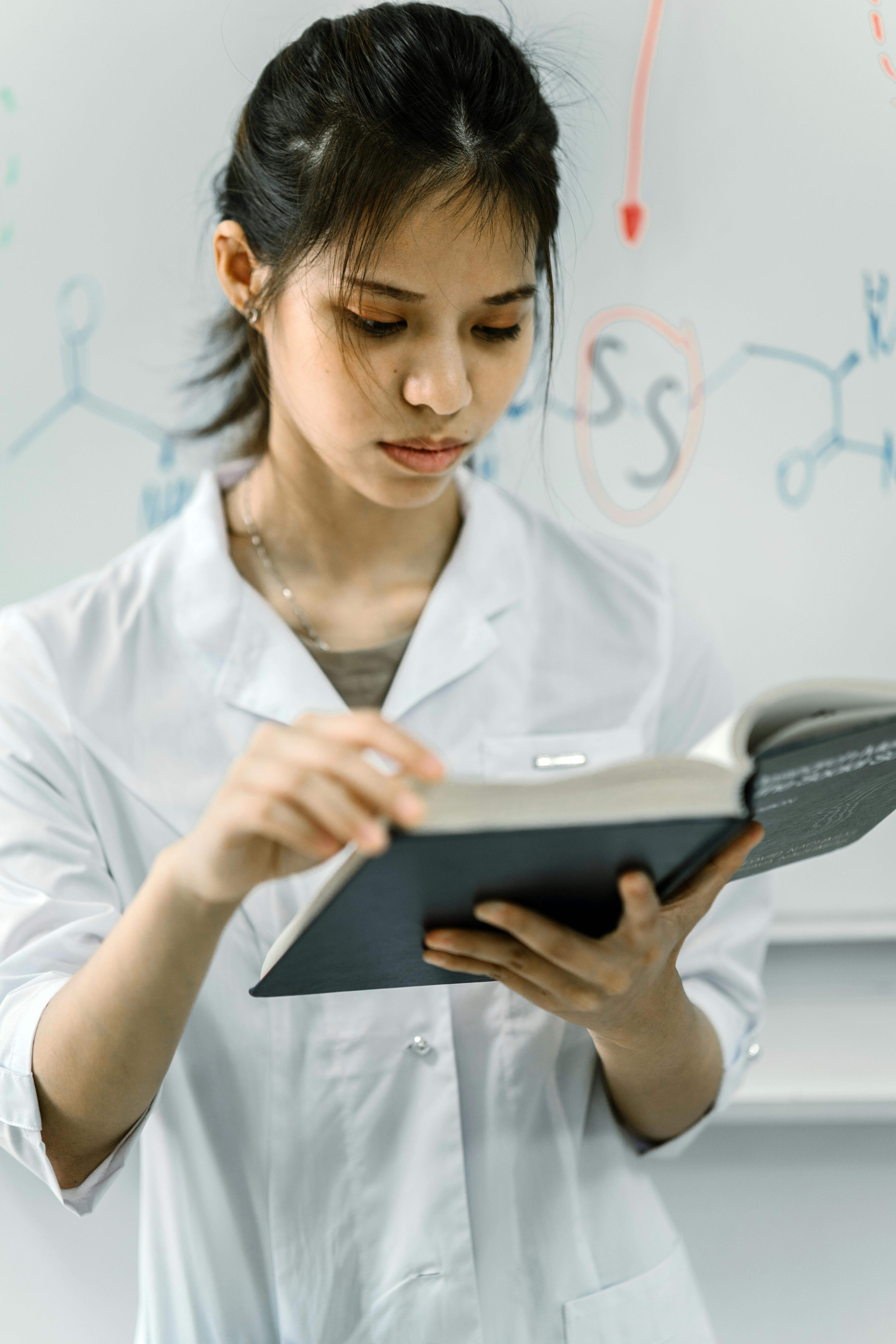 Woman Wearing Laboratory Gown Reading Book · Free Stock Photo