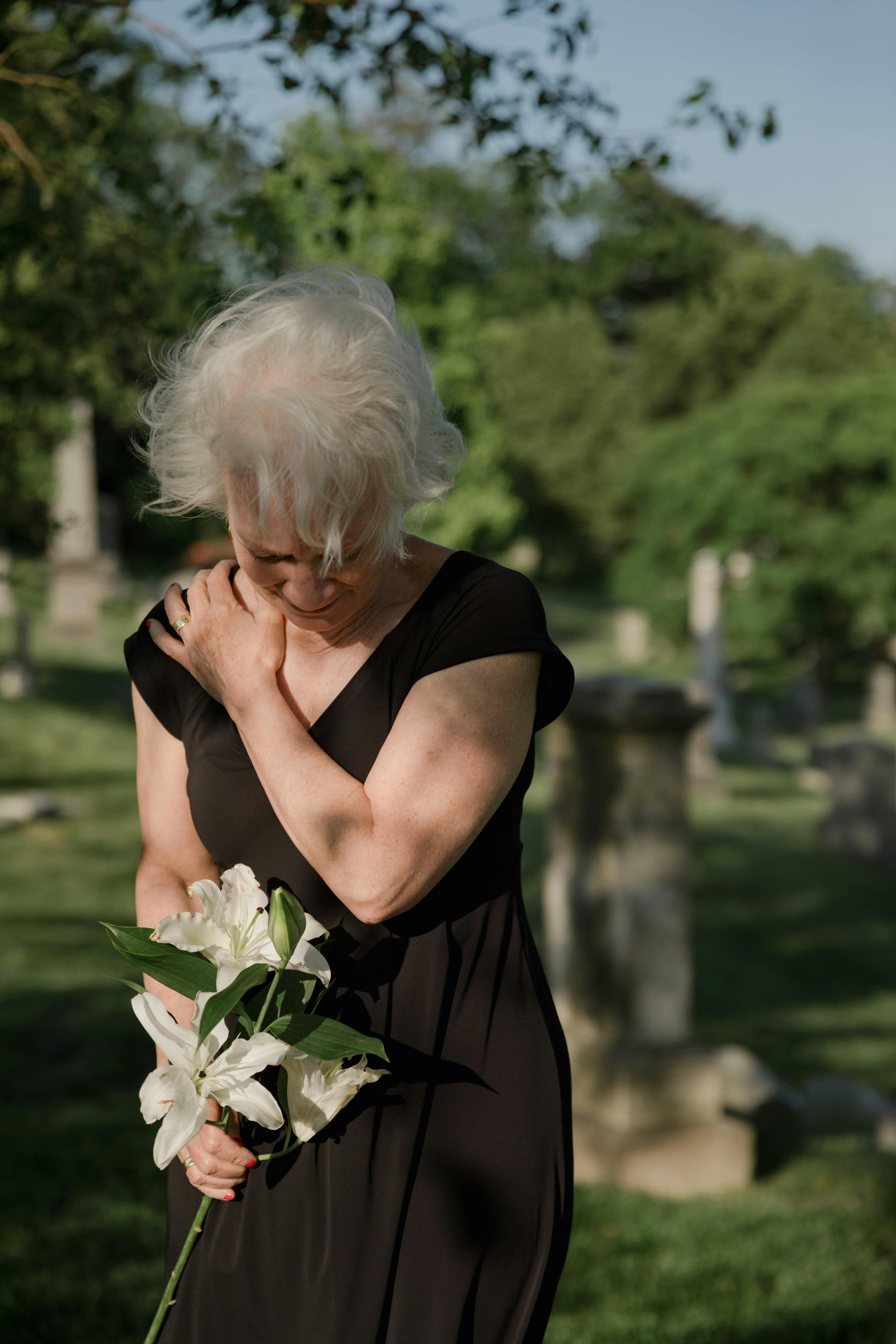 Photo of A Grieving Elderly Woman Holding White Flowers · Free Stock Photo