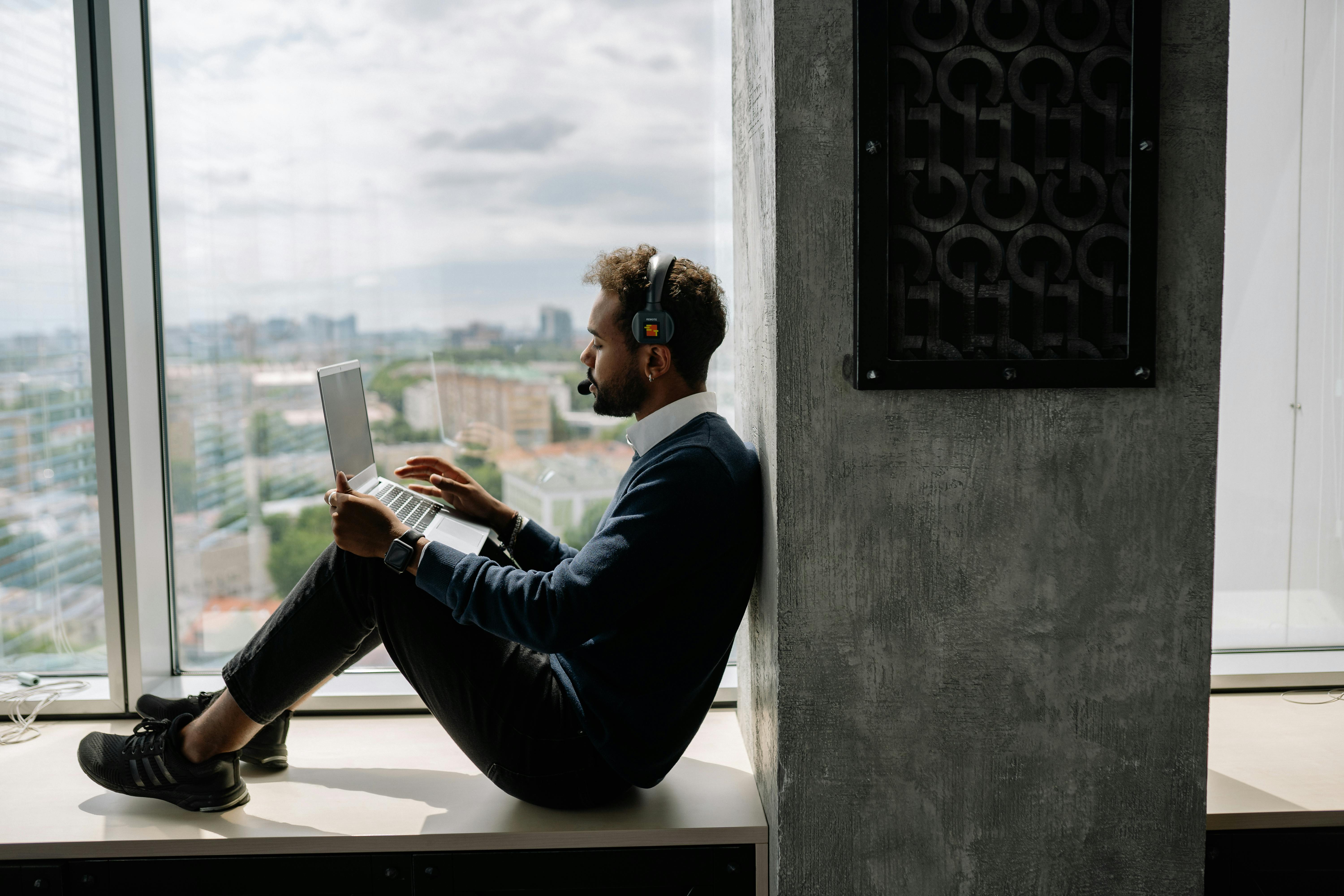 Man Using His Laptop while Sitting on the Window · Free Stock Photo