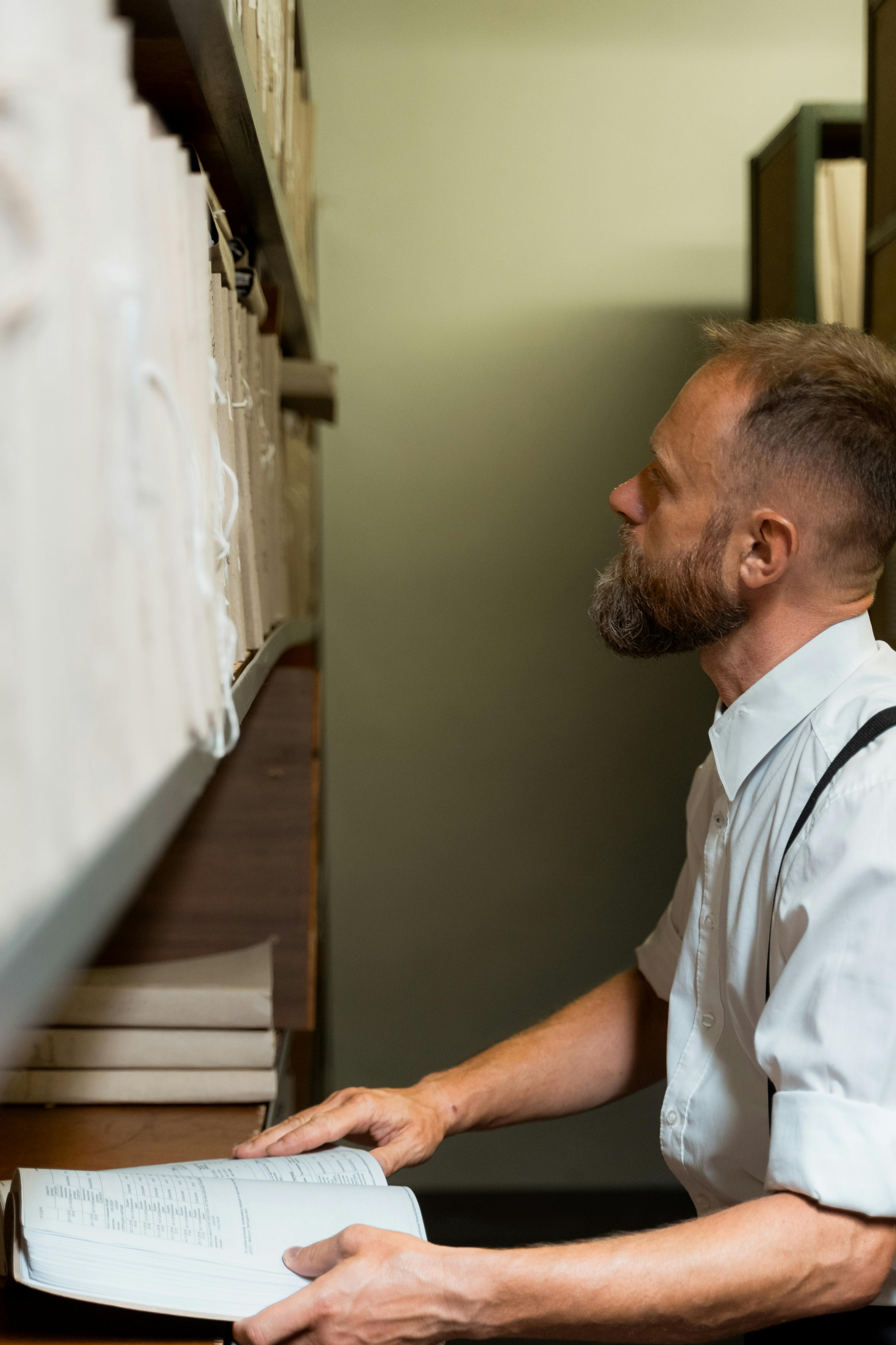 A Man Looking at Files on a Bookshelf · Free Stock Photo