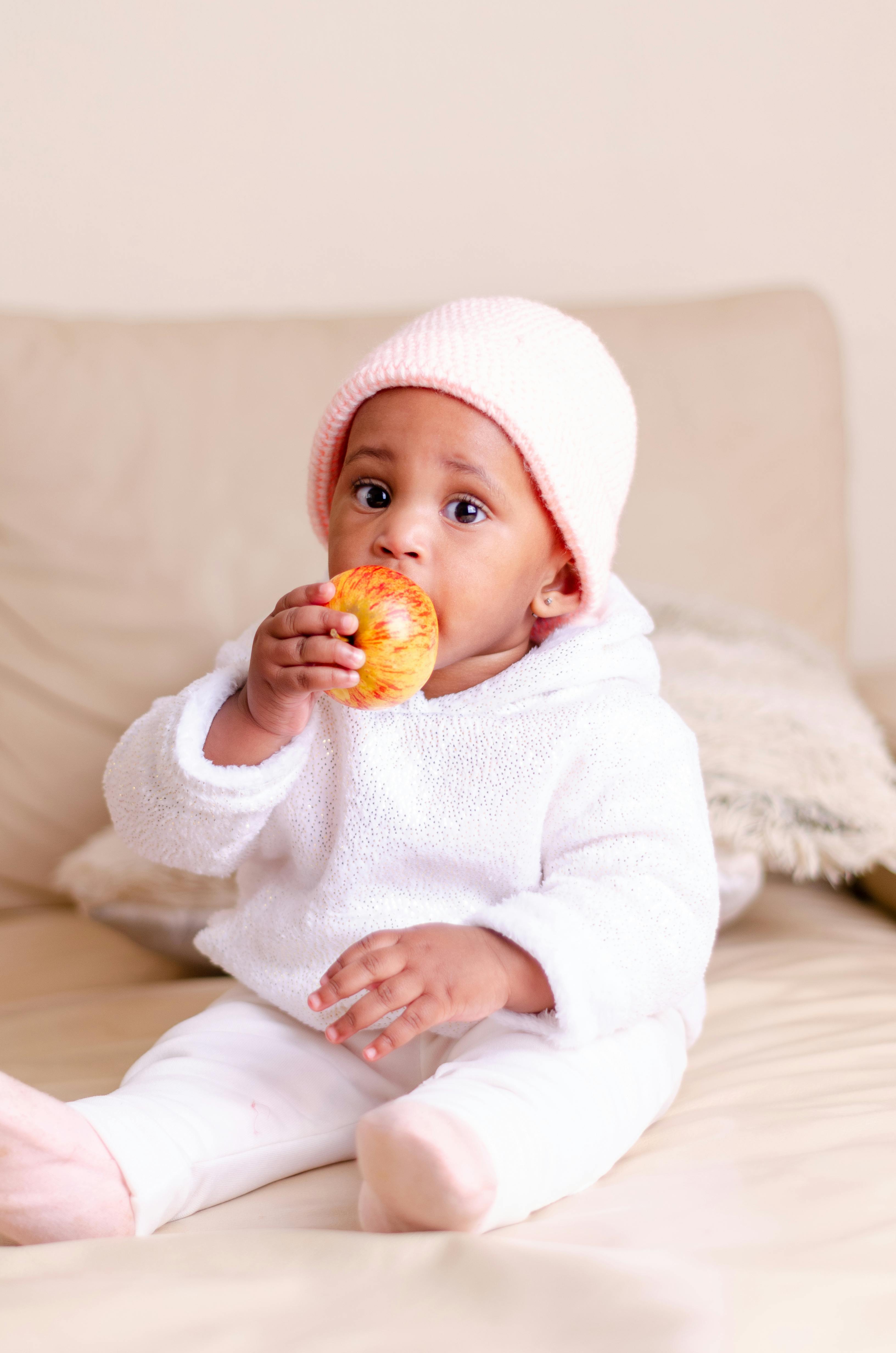 Close-Up Shot of a Cute Baby Holding an Apple while Sitting on Bed ...