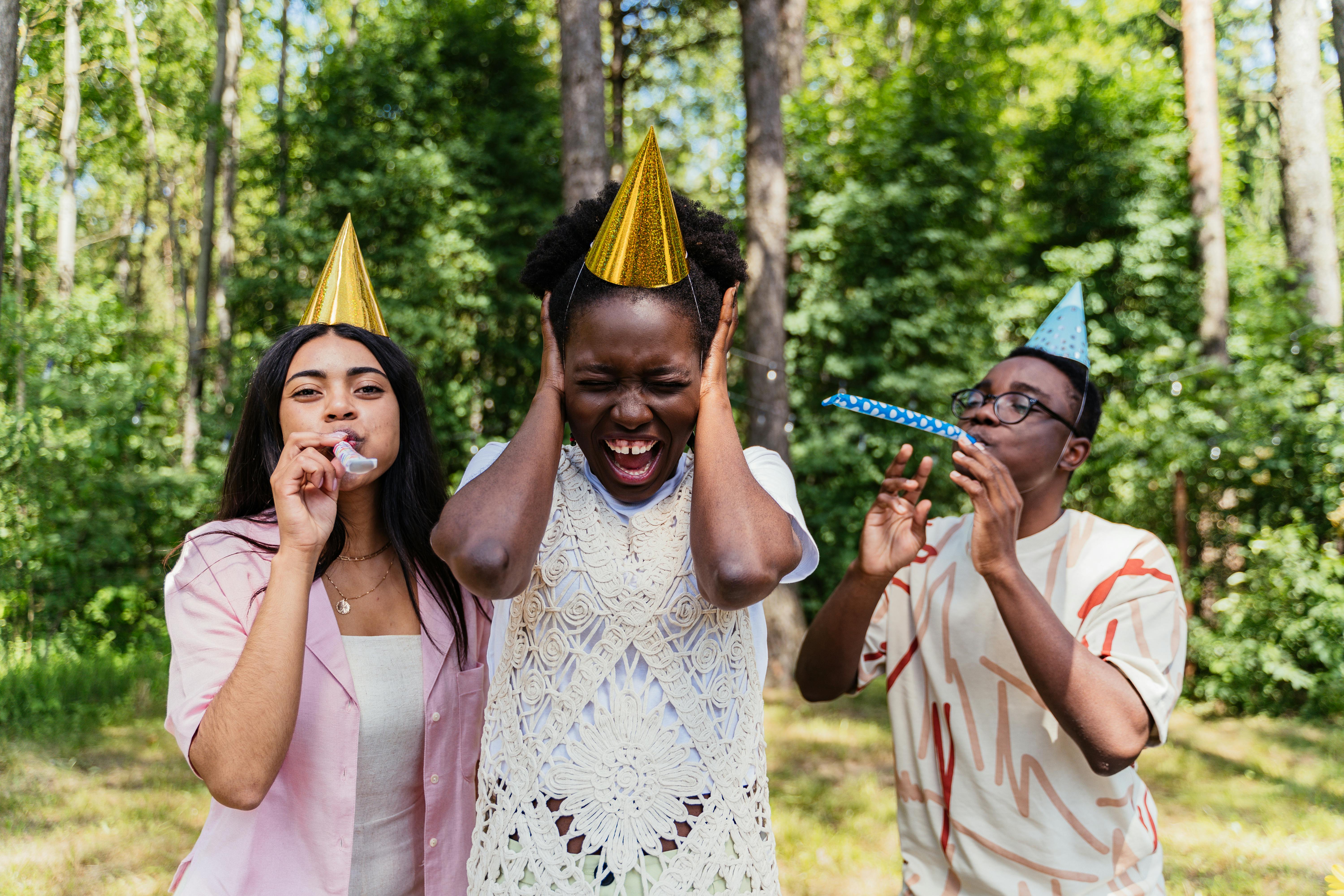 A Young Woman Covering Ears While Friends are Blowing Party Trumpets ...