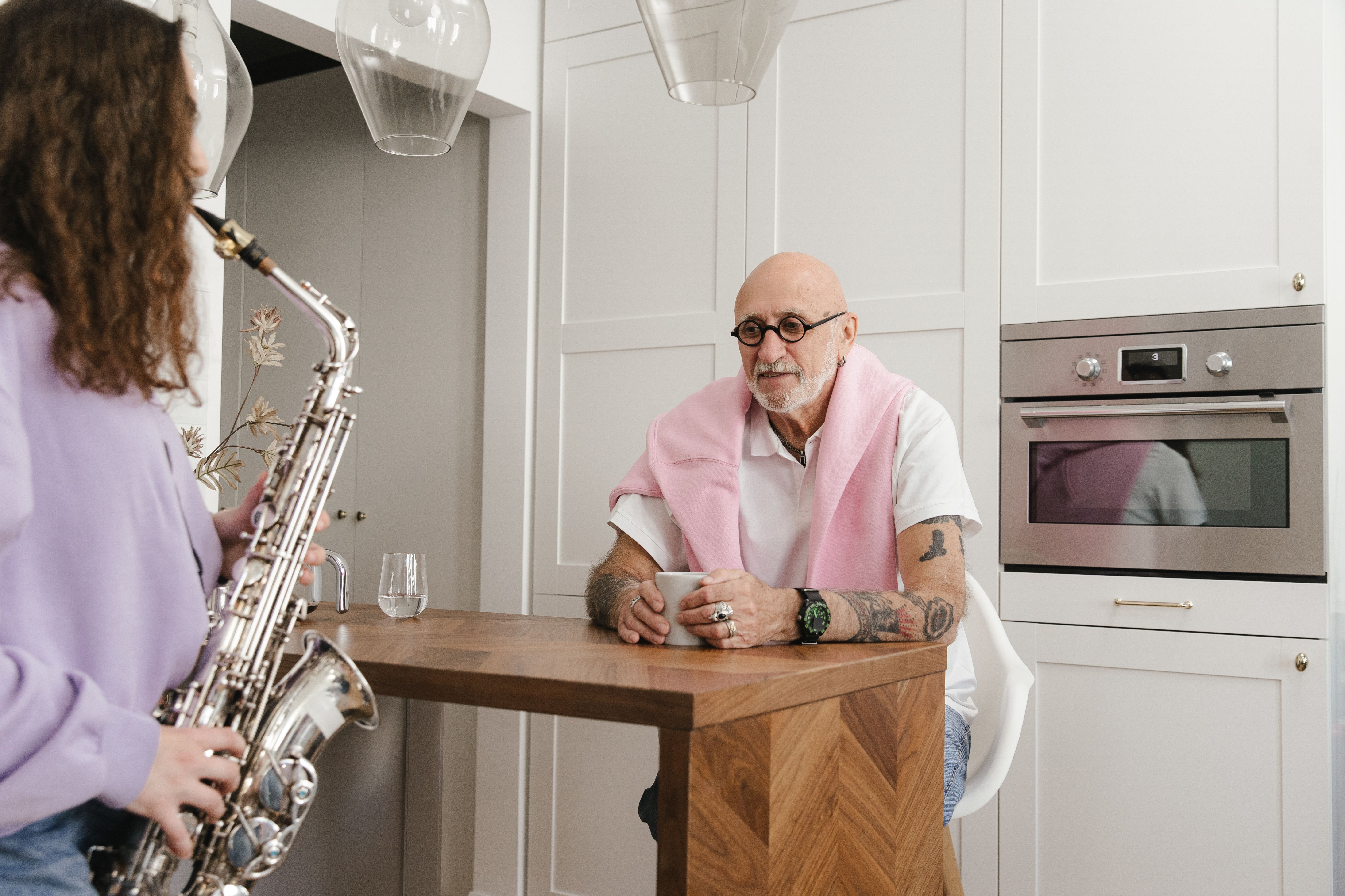 A Woman Playing Saxophone with a Man at the Table While in the Kitchen ...