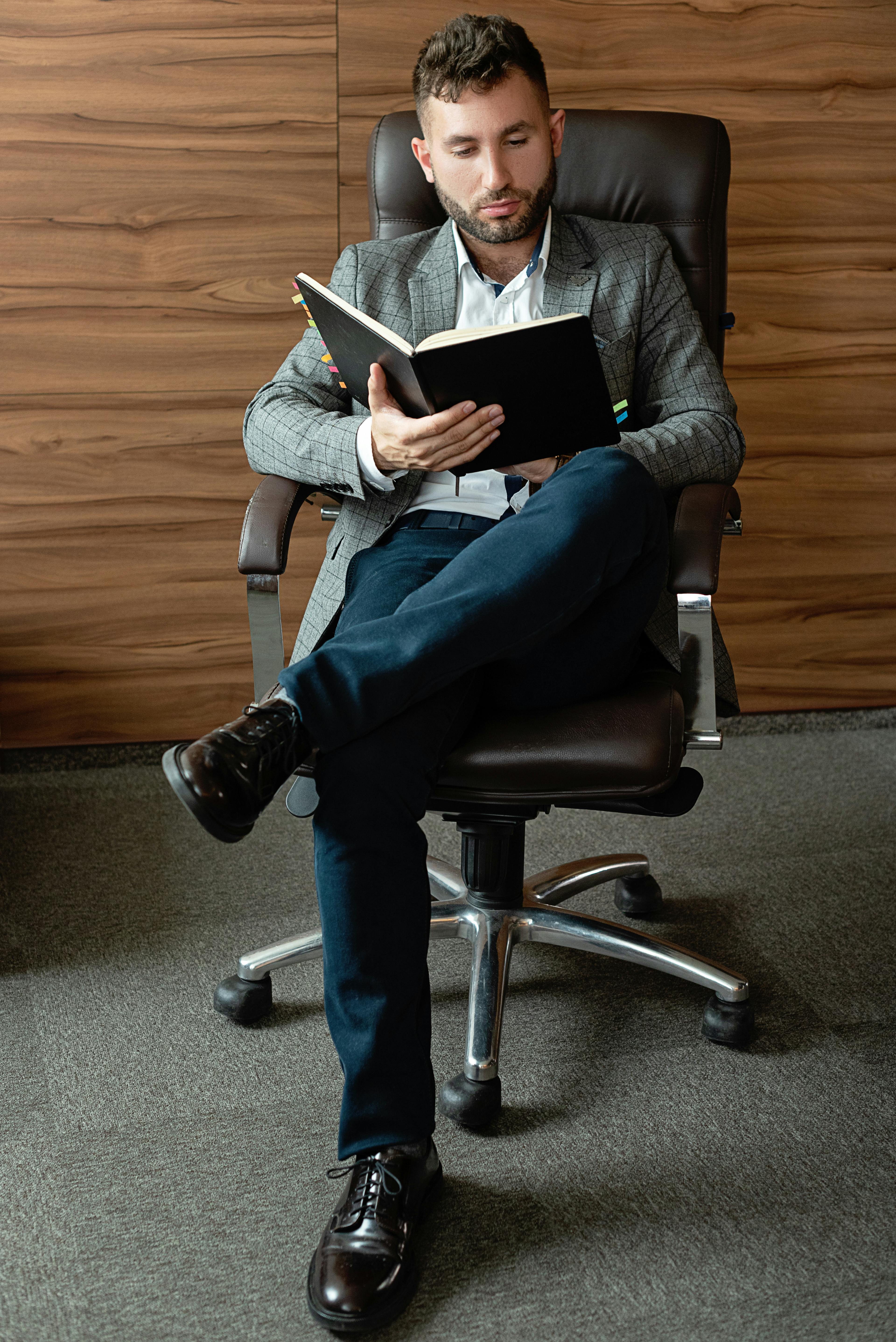 Man Sitting on the Office Chair while Holding a Book · Free Stock Photo