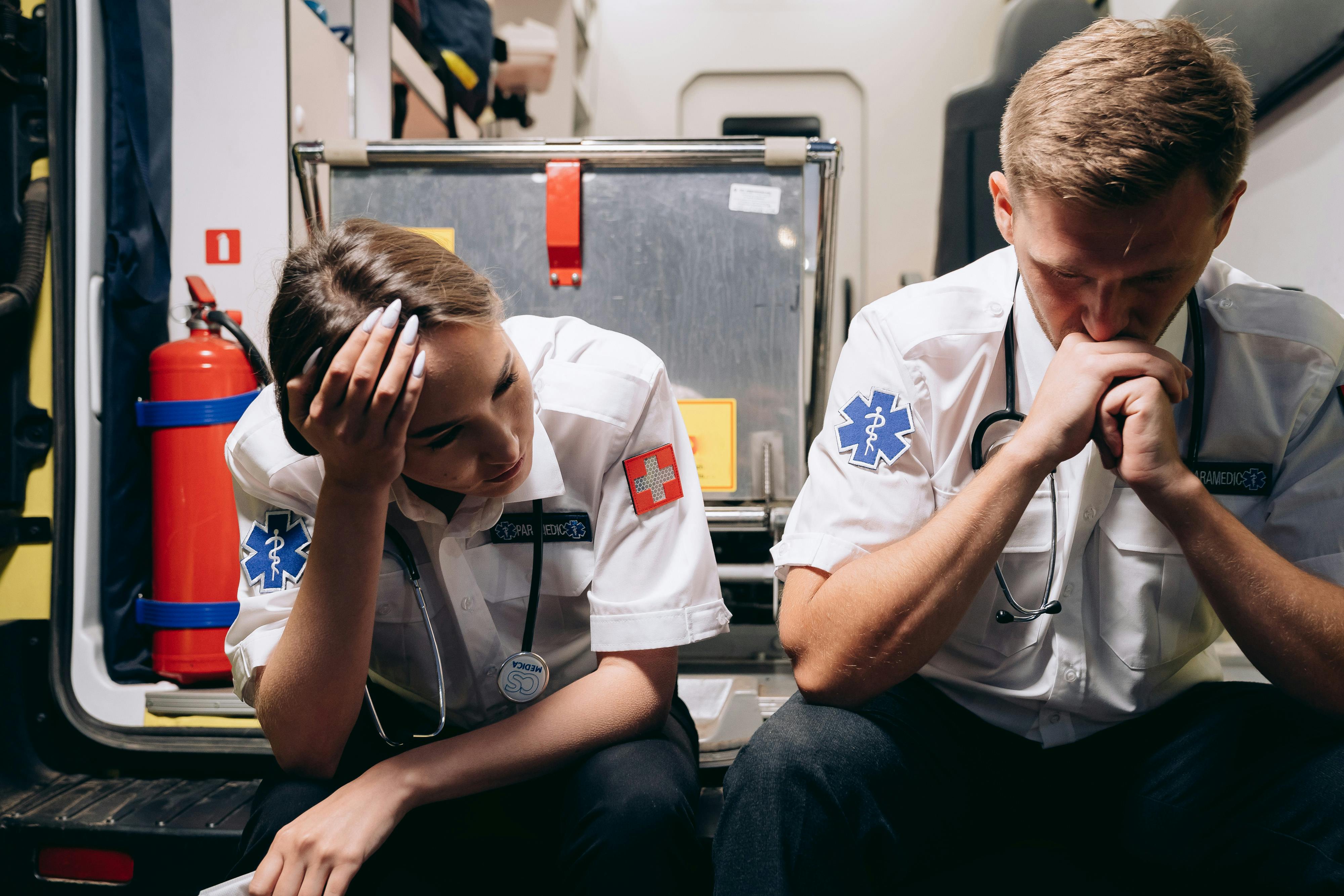 A Pair of Paramedics Sitting on Ambulance Bumper with Regretful ...