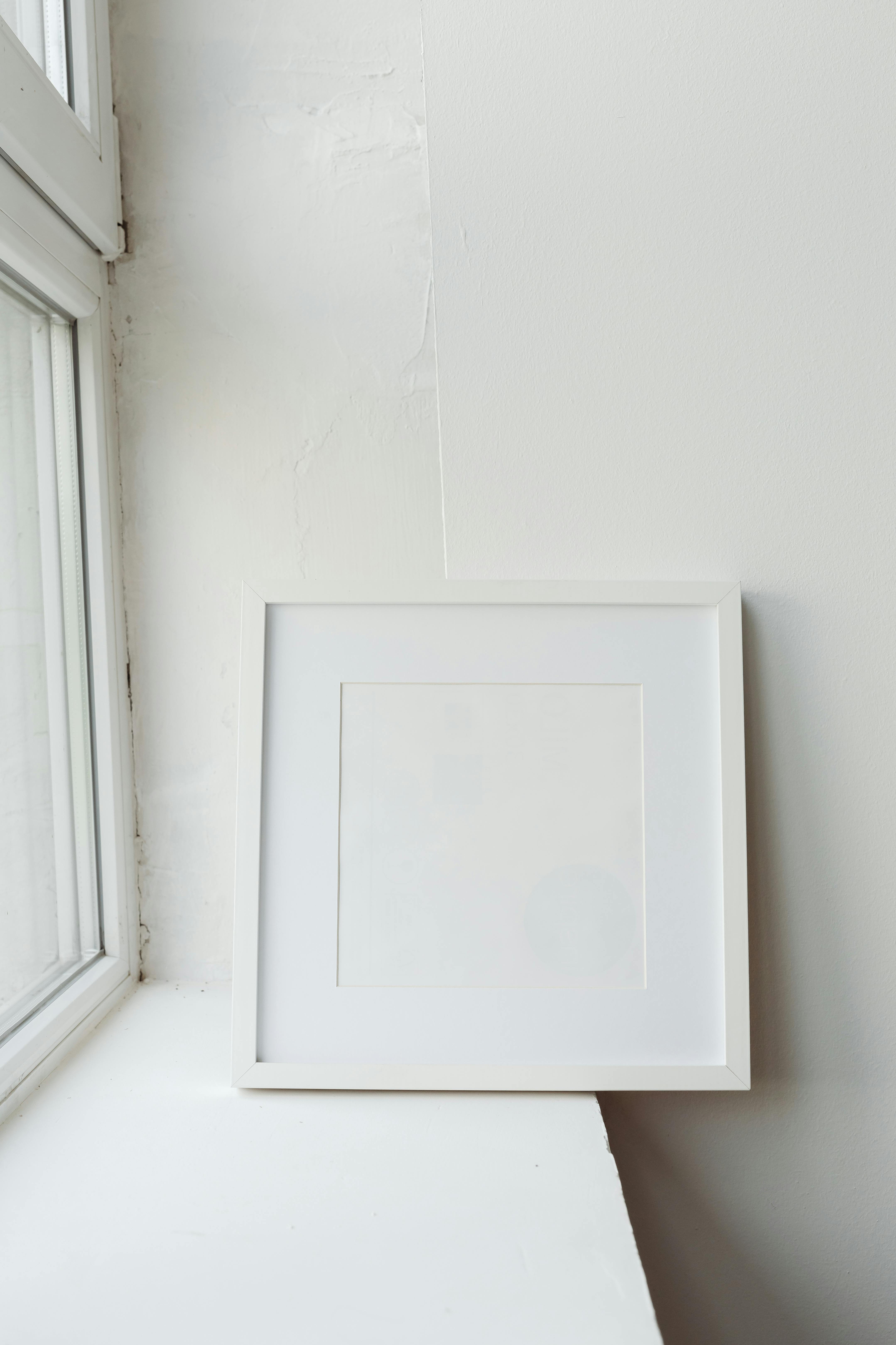 Modern simple frame hanging on wall between windows · Free Stock Photo