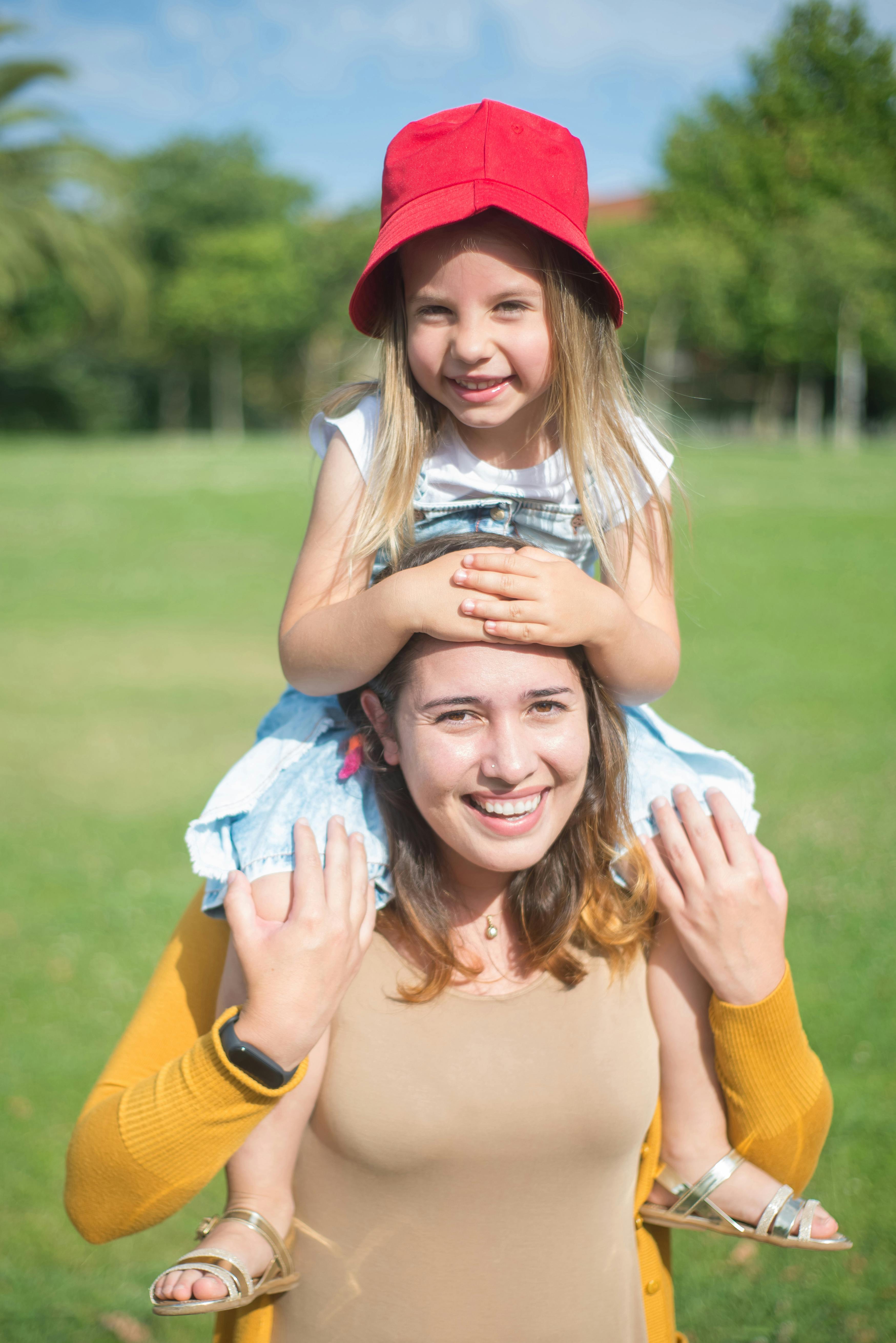 Girl in Red Hat Sitting on Woman's Shoulder · Free Stock Photo