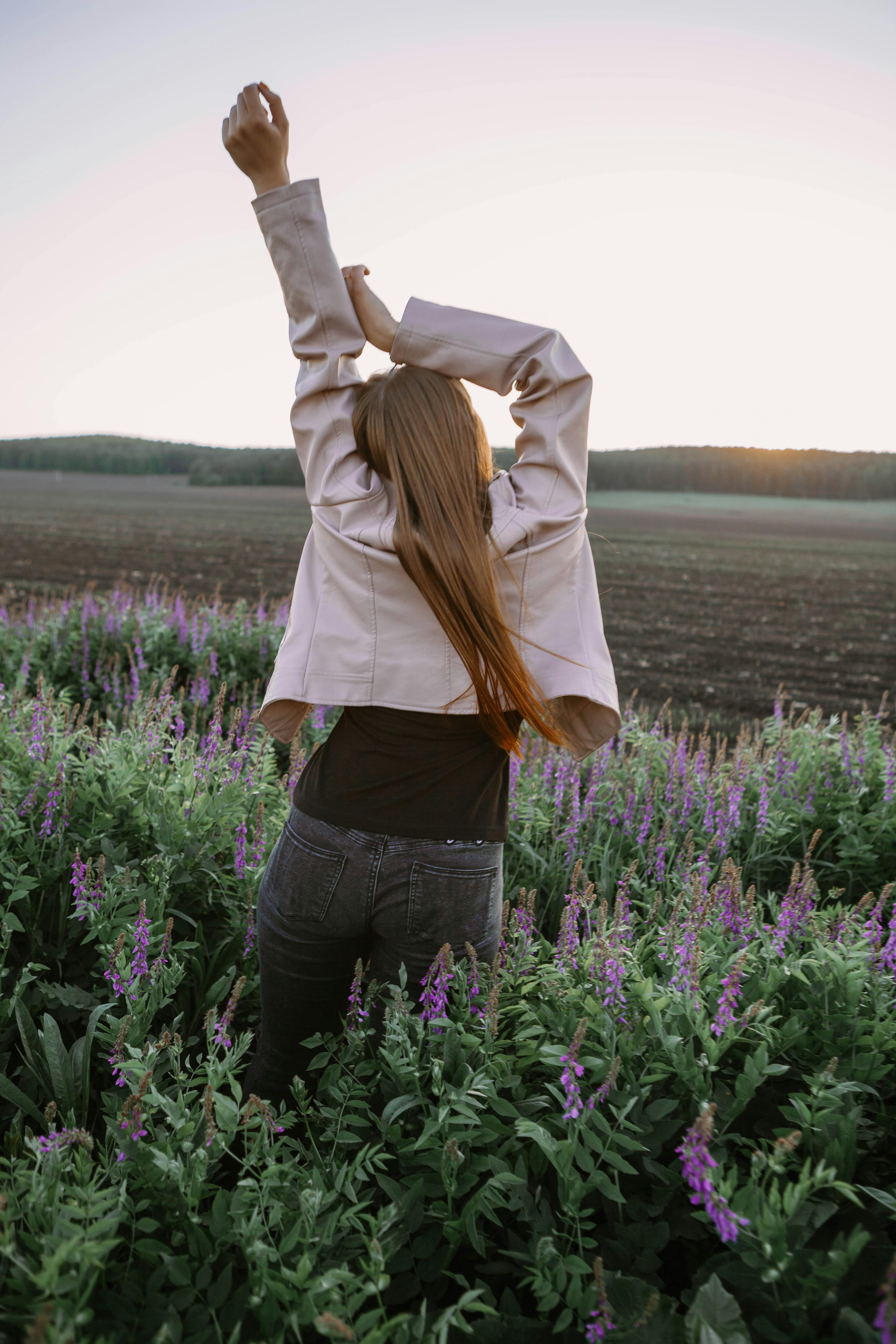 Back View of a Woman with Her Arms Raised on a Field · Free Stock Photo
