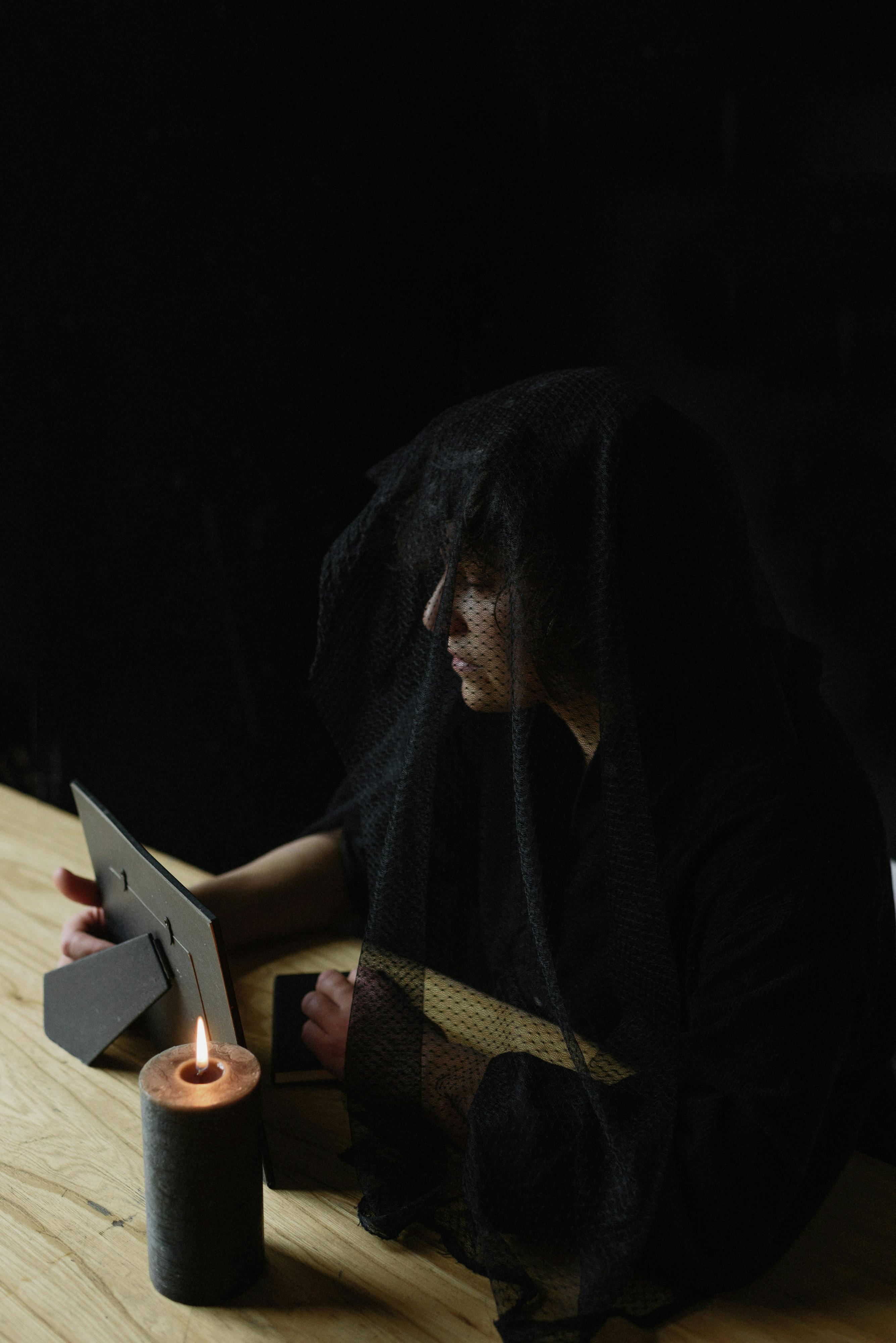 Black Image of a Widow Sitting at a Desk with a Candle and Photograph ...