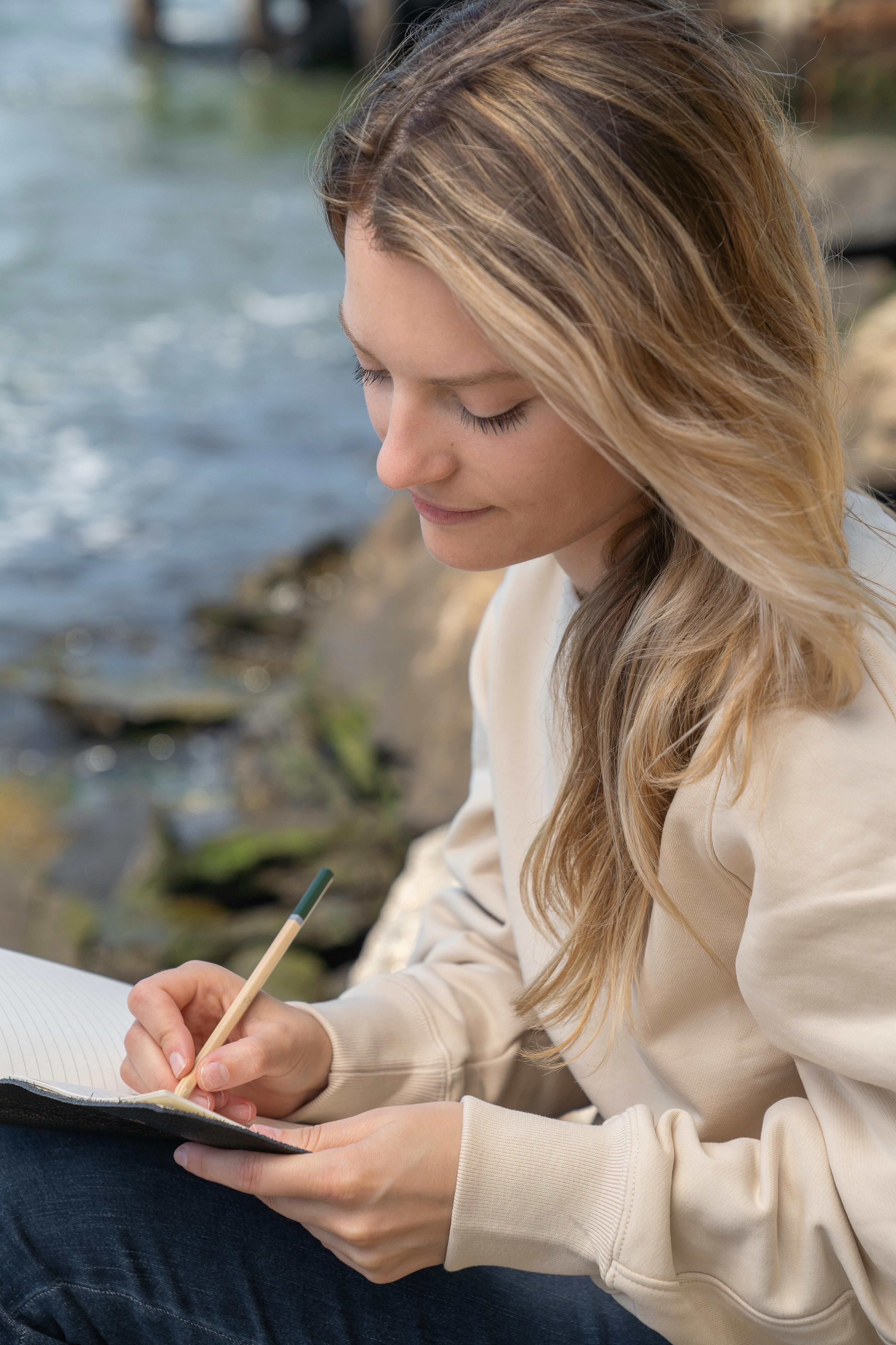 A Beautiful Woman in Beige Sweater Writing on a Notebook · Free Stock Photo