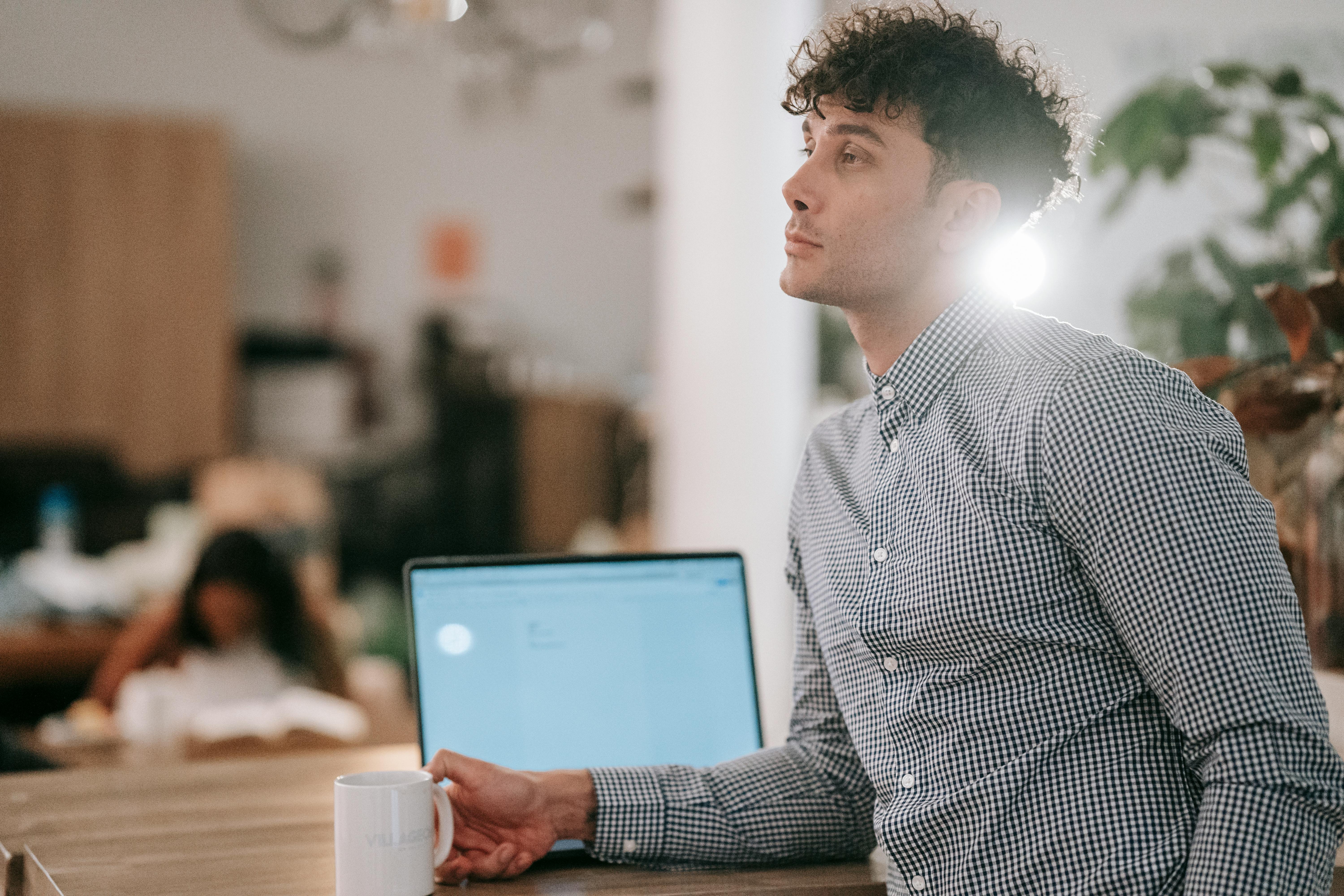 Young Man Sitting with a Cup of Coffee and a Laptop · Free Stock Photo