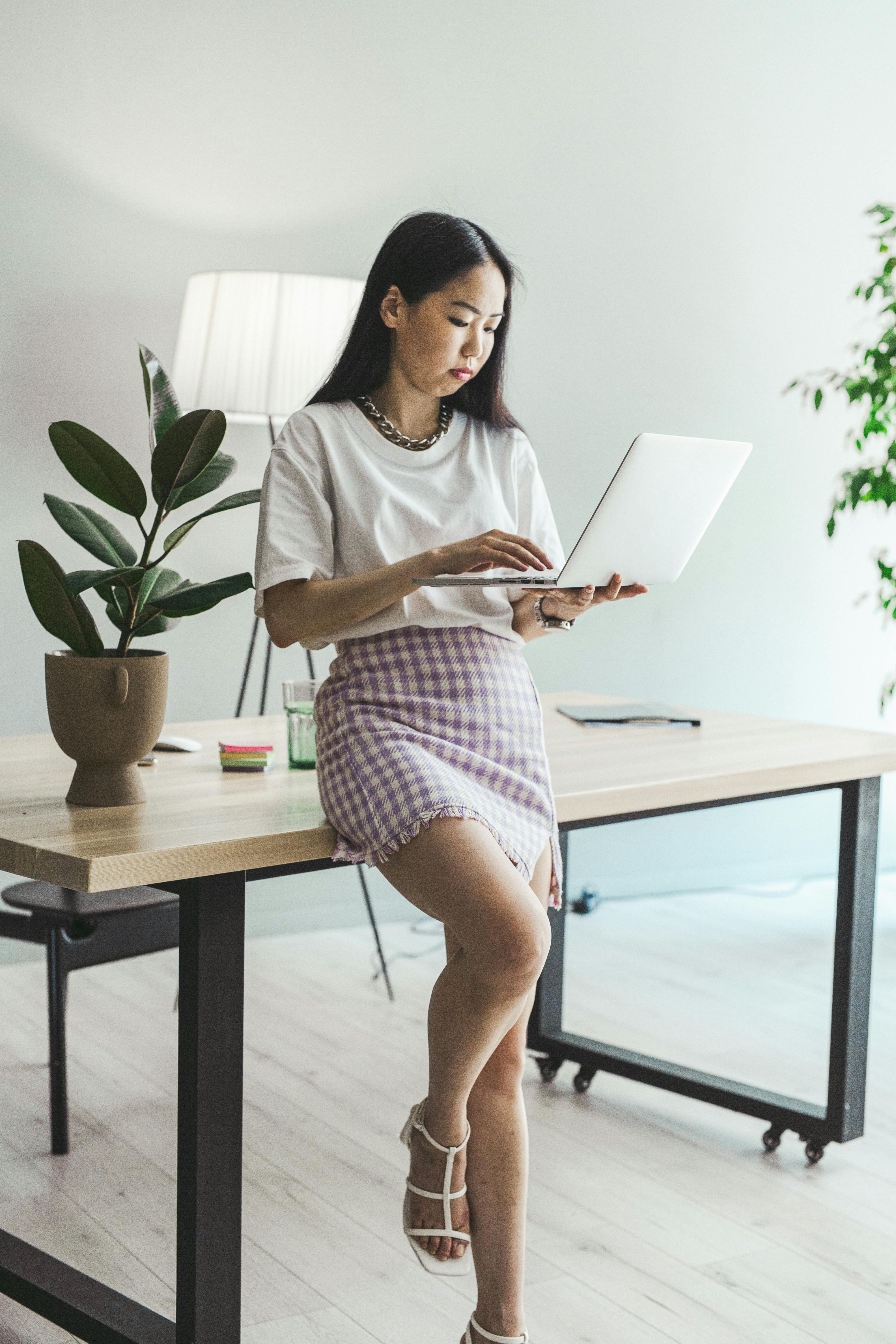 A Woman Using a Laptop while Leaning on a Desk · Free Stock Photo