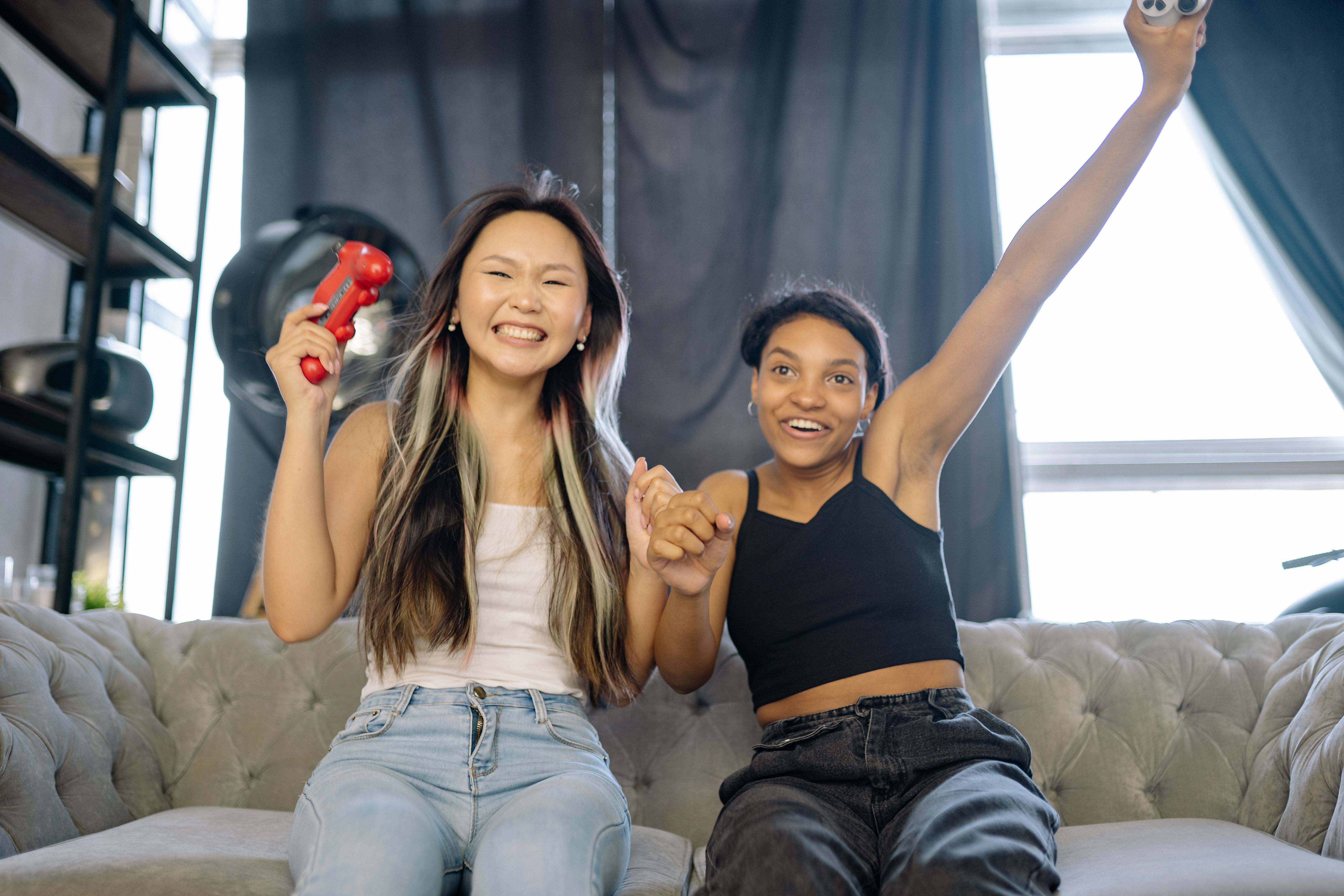 Women Sitting on Sofa Holding Game Controllers Cheering · Free Stock Photo