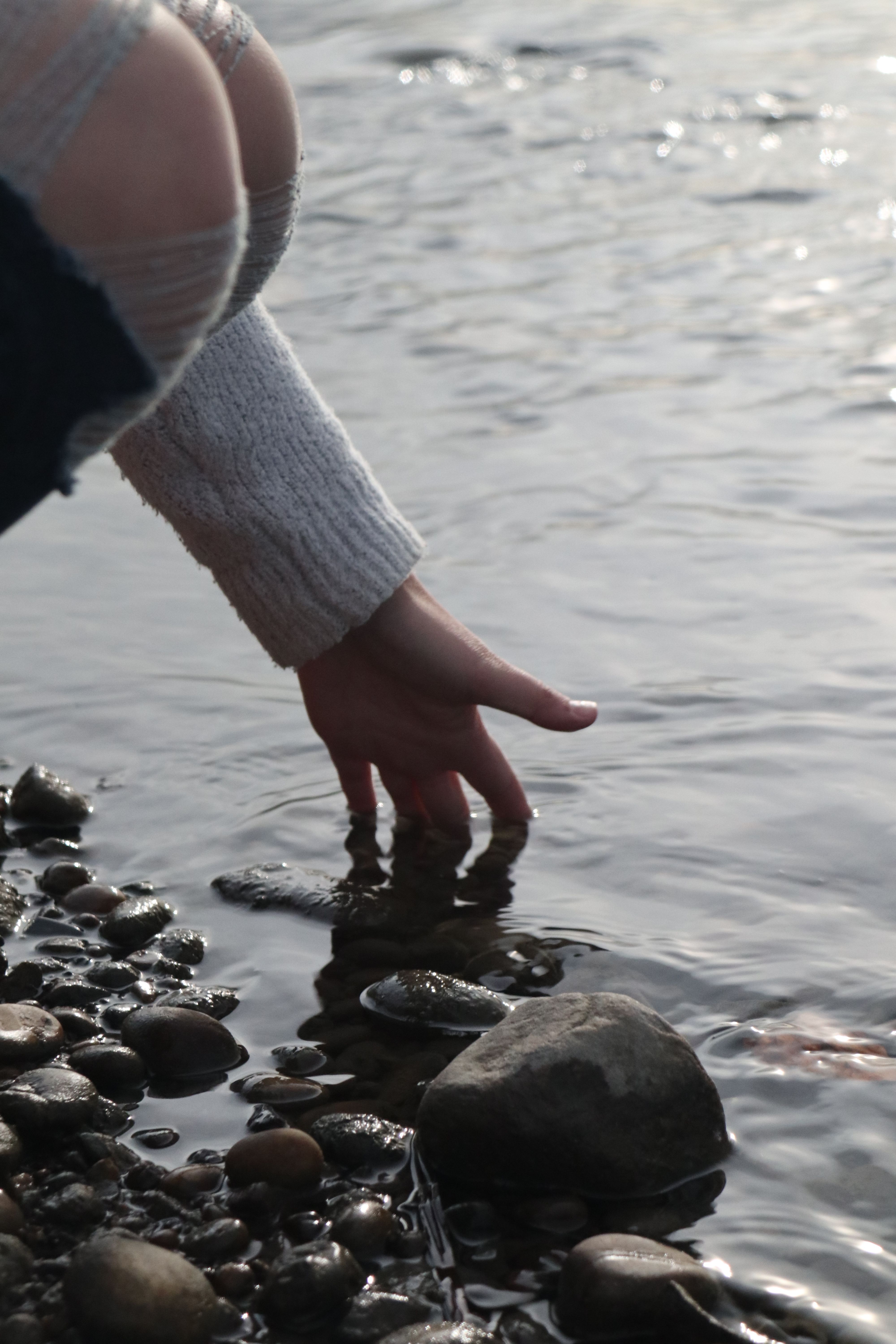 A Person Touching the Water on a Rocky Shore · Free Stock Photo
