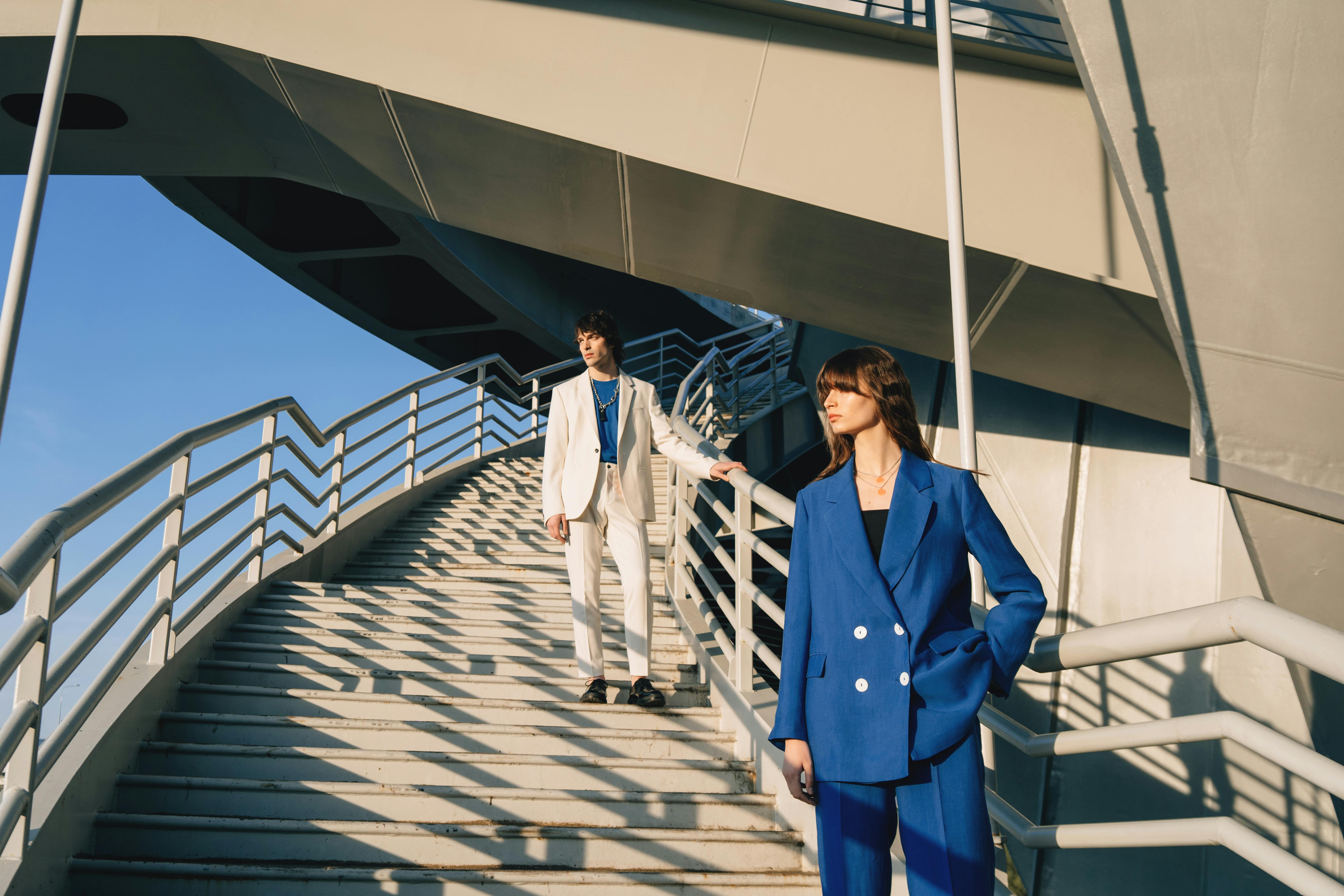 Woman in a Blue Suit and a Man in a White Suit Standing on a Staircase ...
