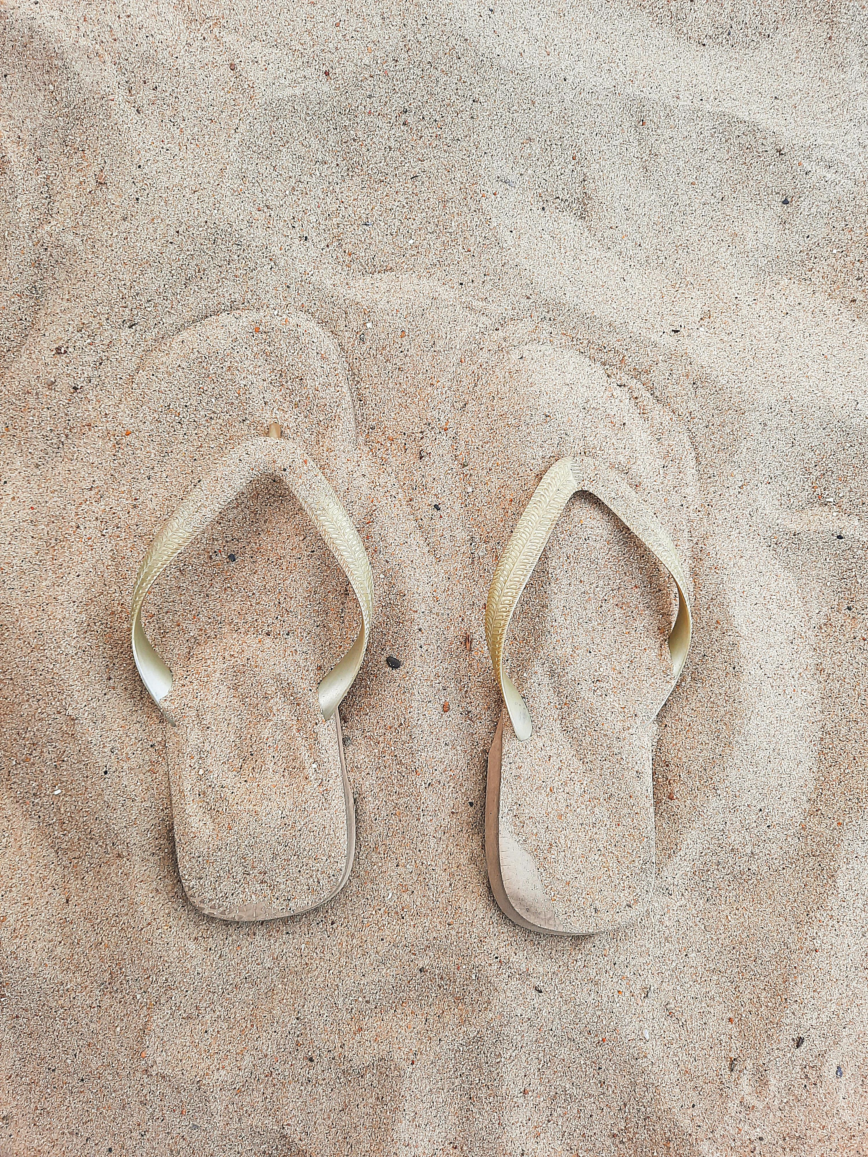 A Pair of White Flip Flops Covered with Sand · Free Stock Photo