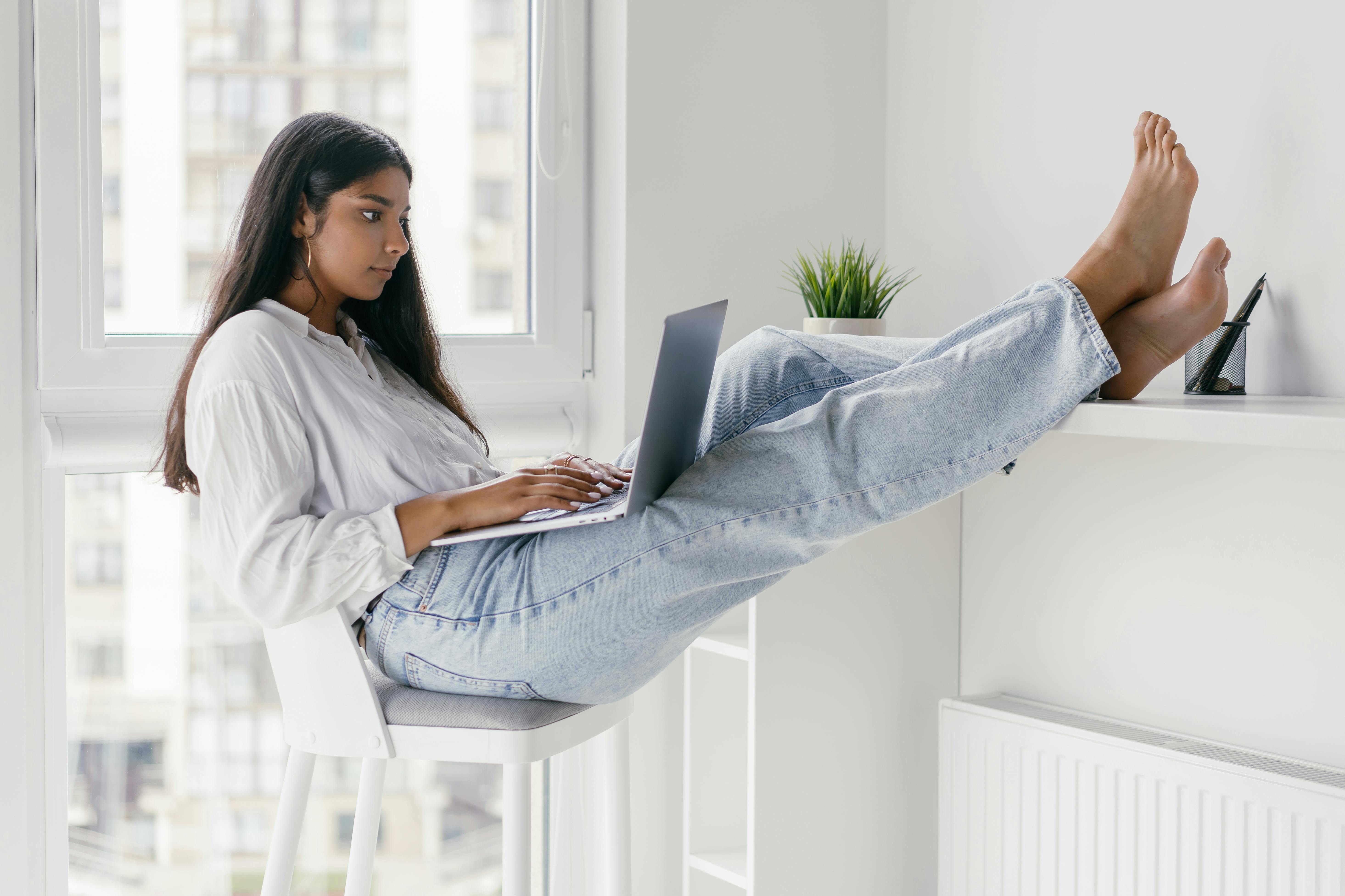 A Woman Sitting on a Stool While Using a Laptop · Free Stock Photo