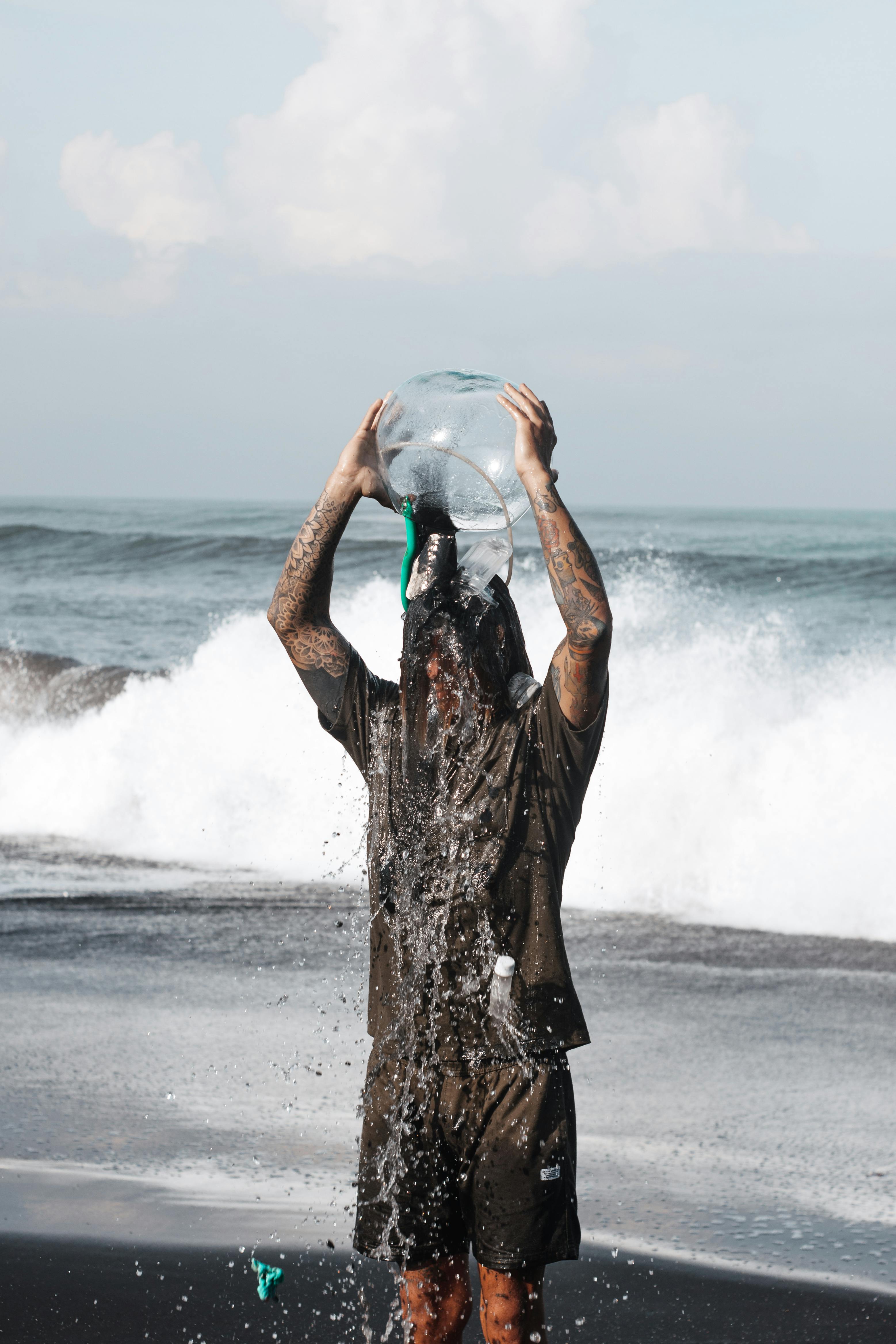 Man Pouring Water from Glass Jar on Beach · Free Stock Photo