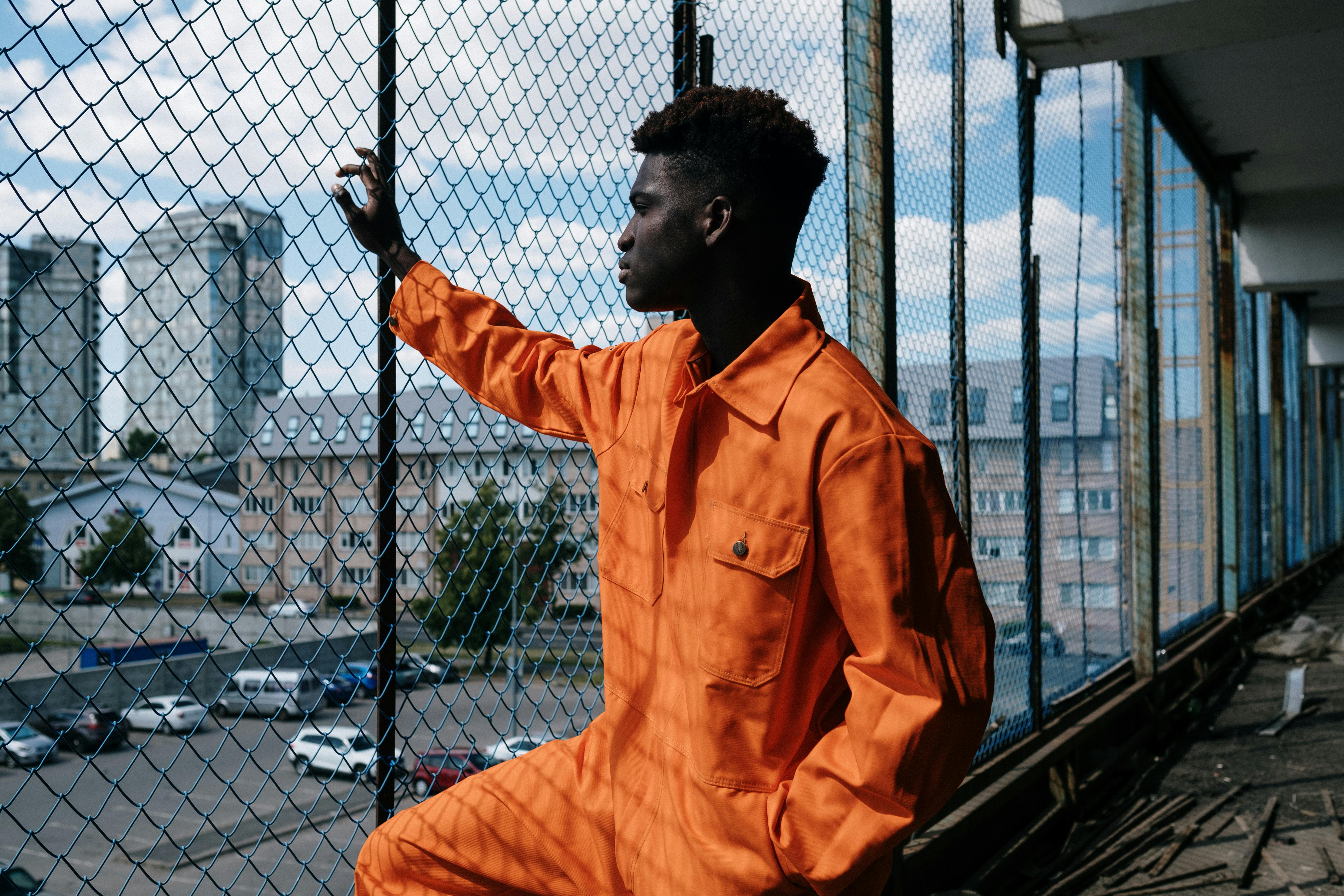 Man in Orange Overalls Looking through Fence · Free Stock Photo