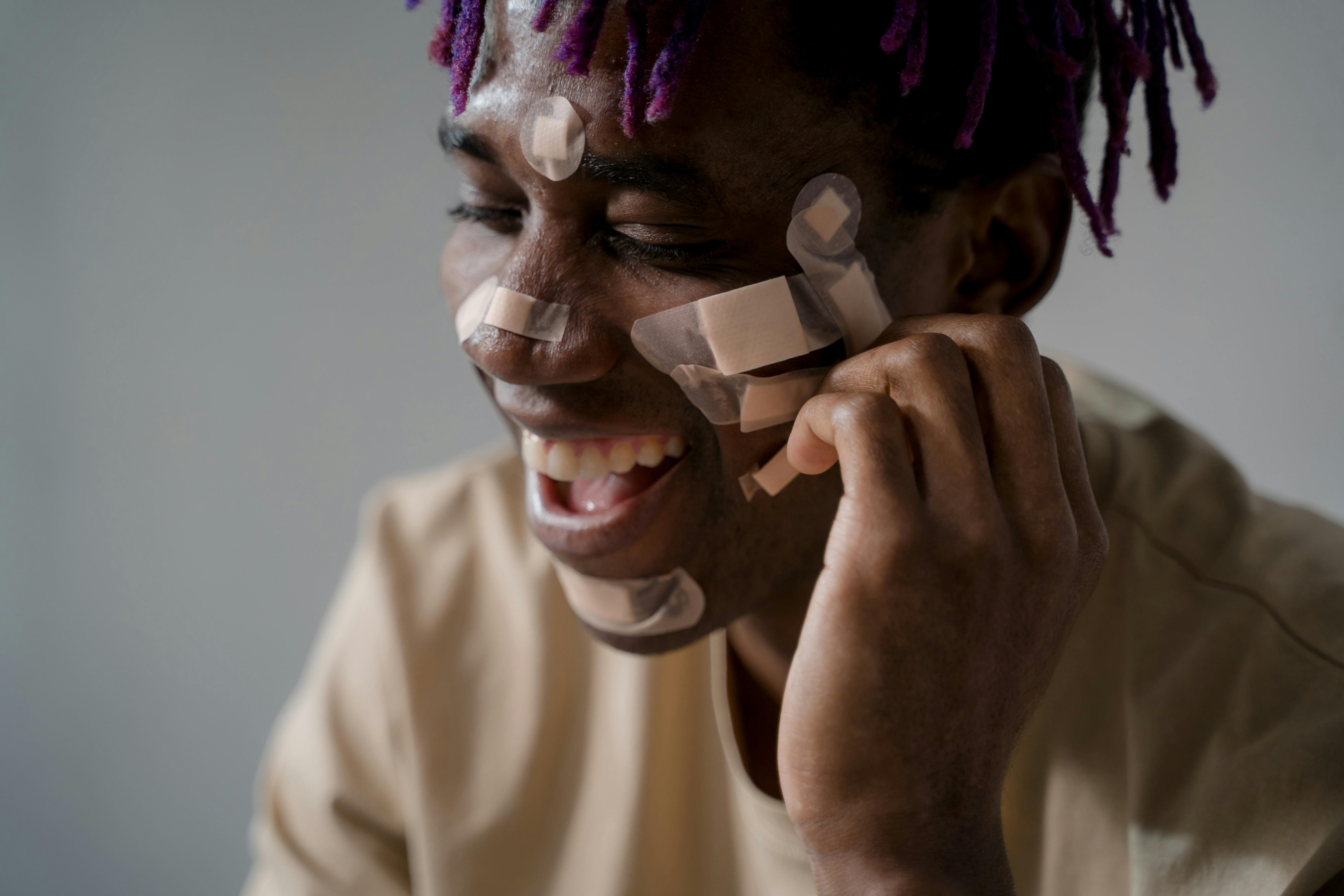 Young Man with a Smile Peeling Plasters from His Face · Free Stock Photo