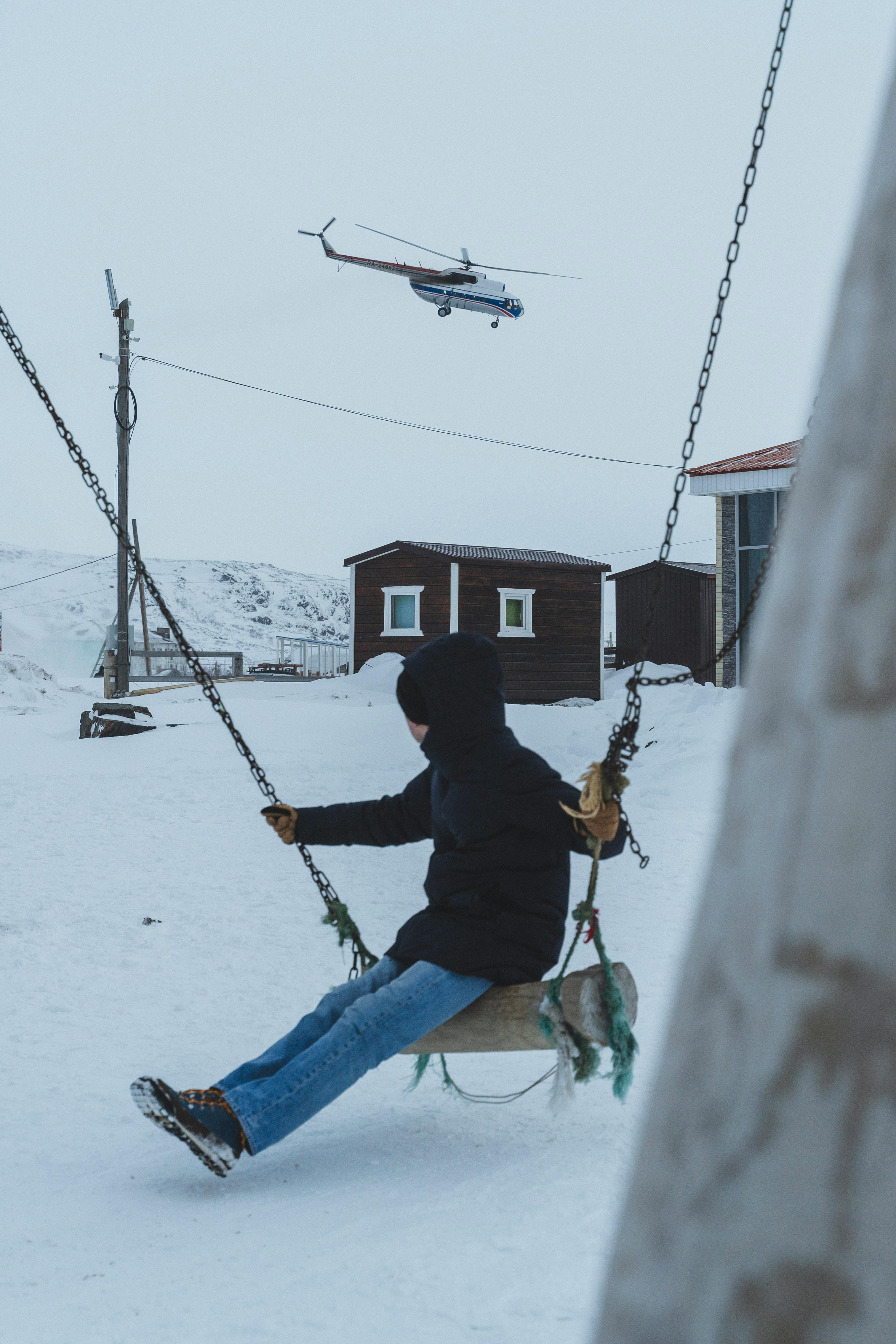 A Child Sitting at a Swing while Looking at a Helicopter · Free Stock Photo