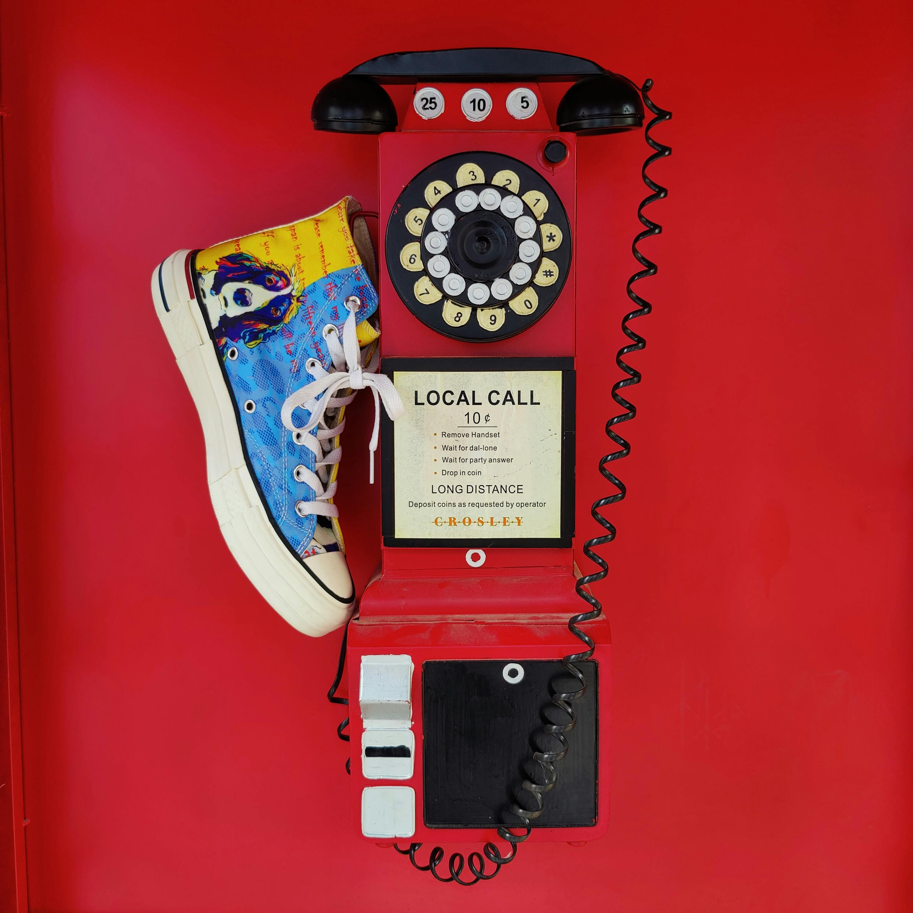 Vintage Payphone and a Shoe on Red Background · Free Stock Photo
