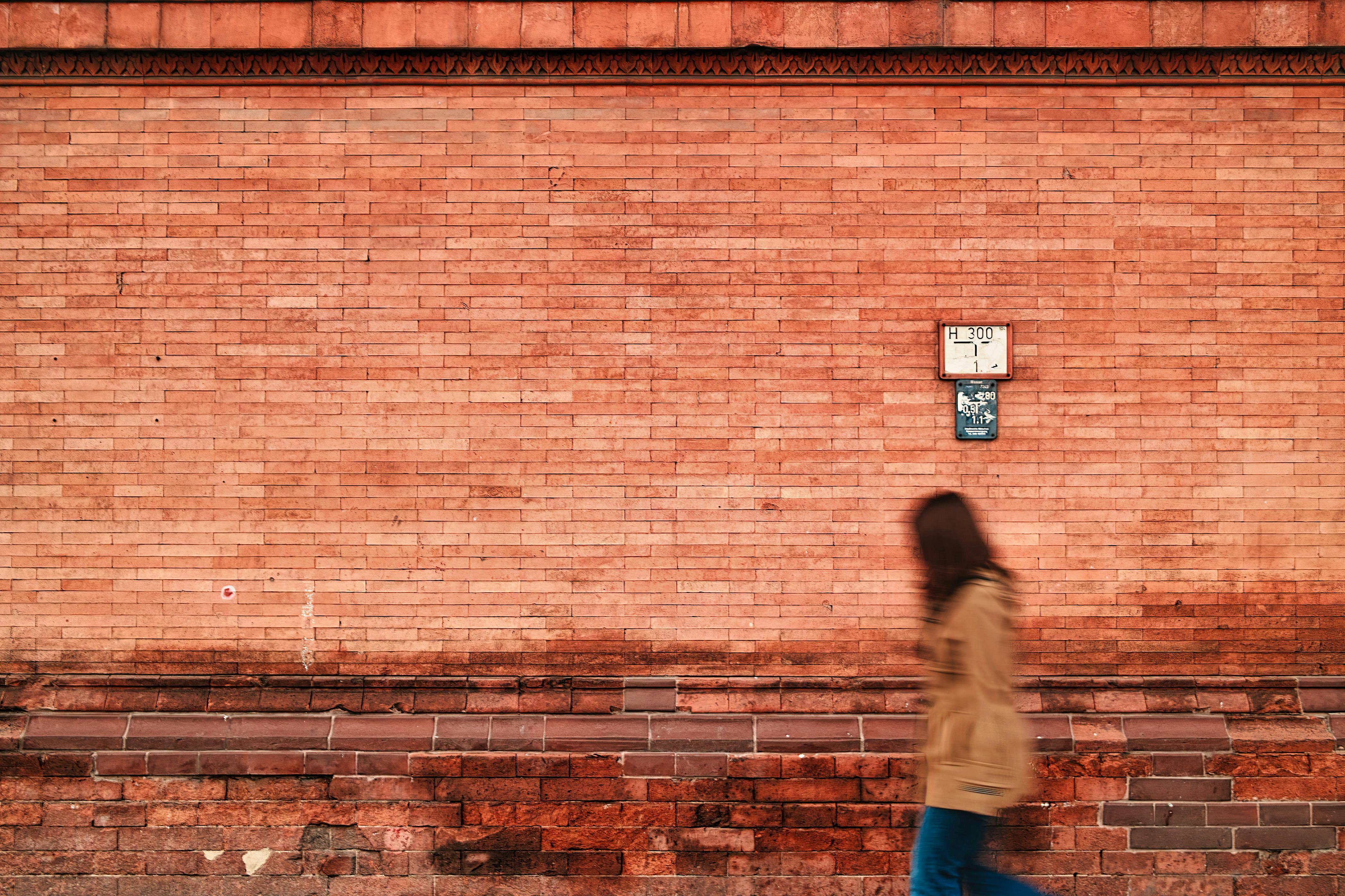 A Woman Walking Past a Brick Wall · Free Stock Photo