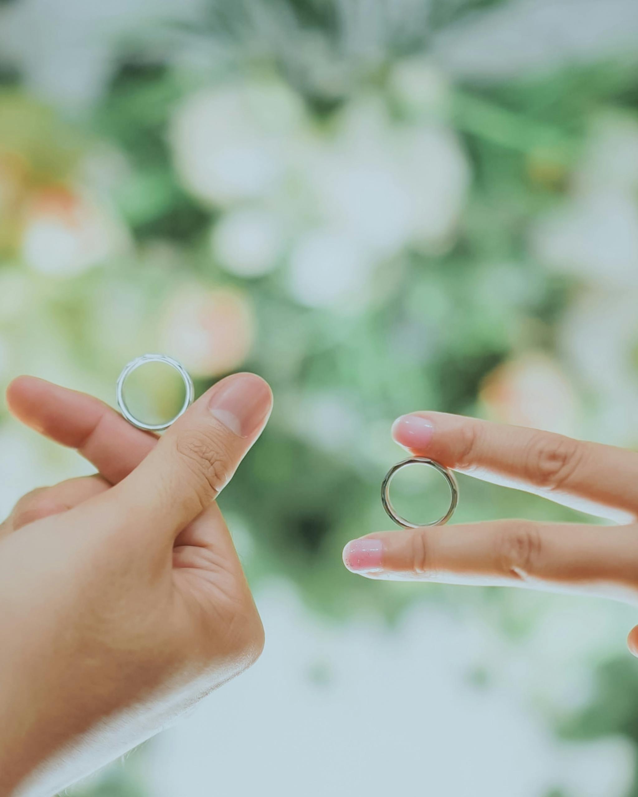 Selective Focus Photo of Two Hands Holding Wedding Rings · Free Stock Photo