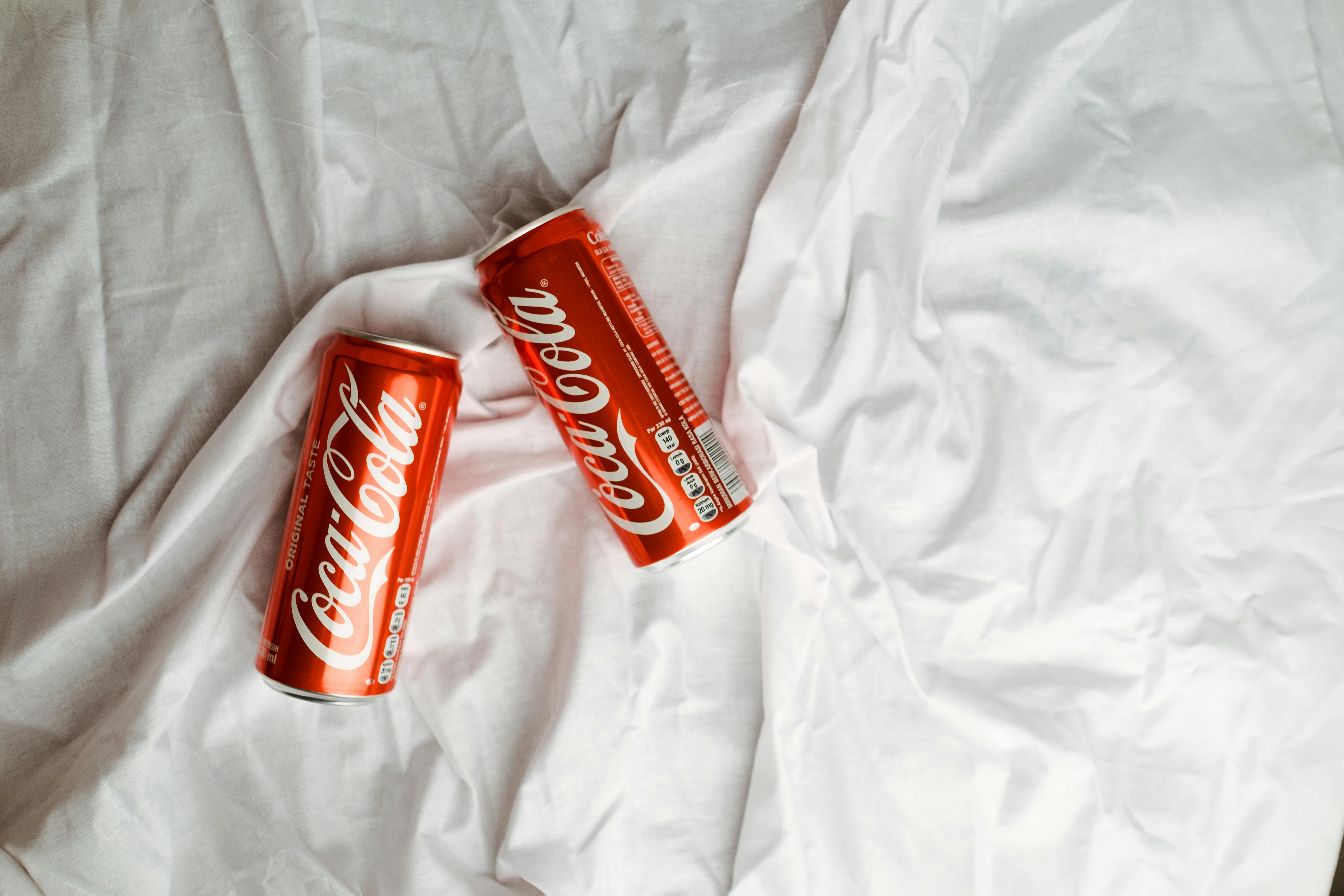 Coca Cola Cans on White Textile · Free Stock Photo