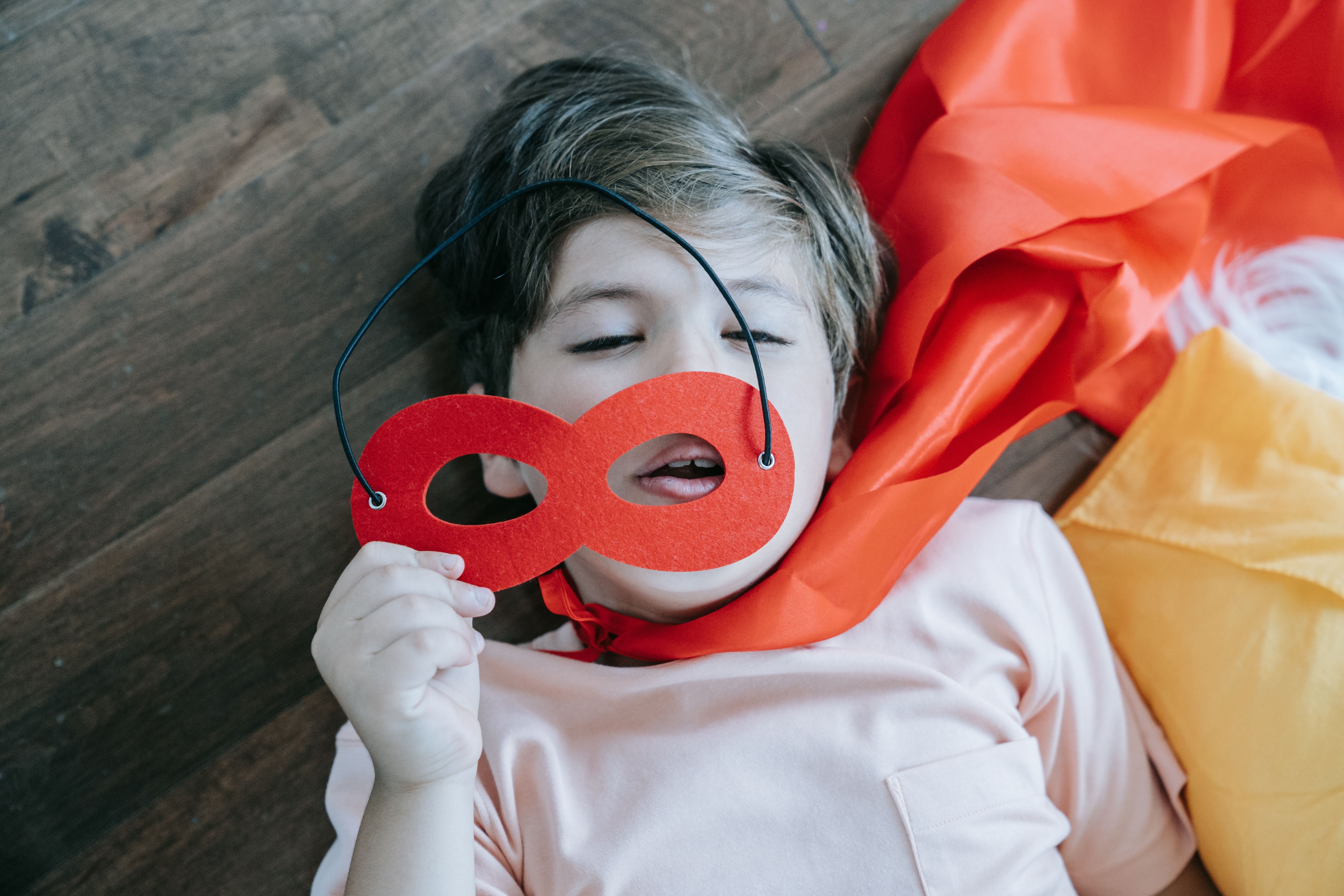 Boy holding a Red Eye Mask lying on Wooden Floor · Free Stock Photo