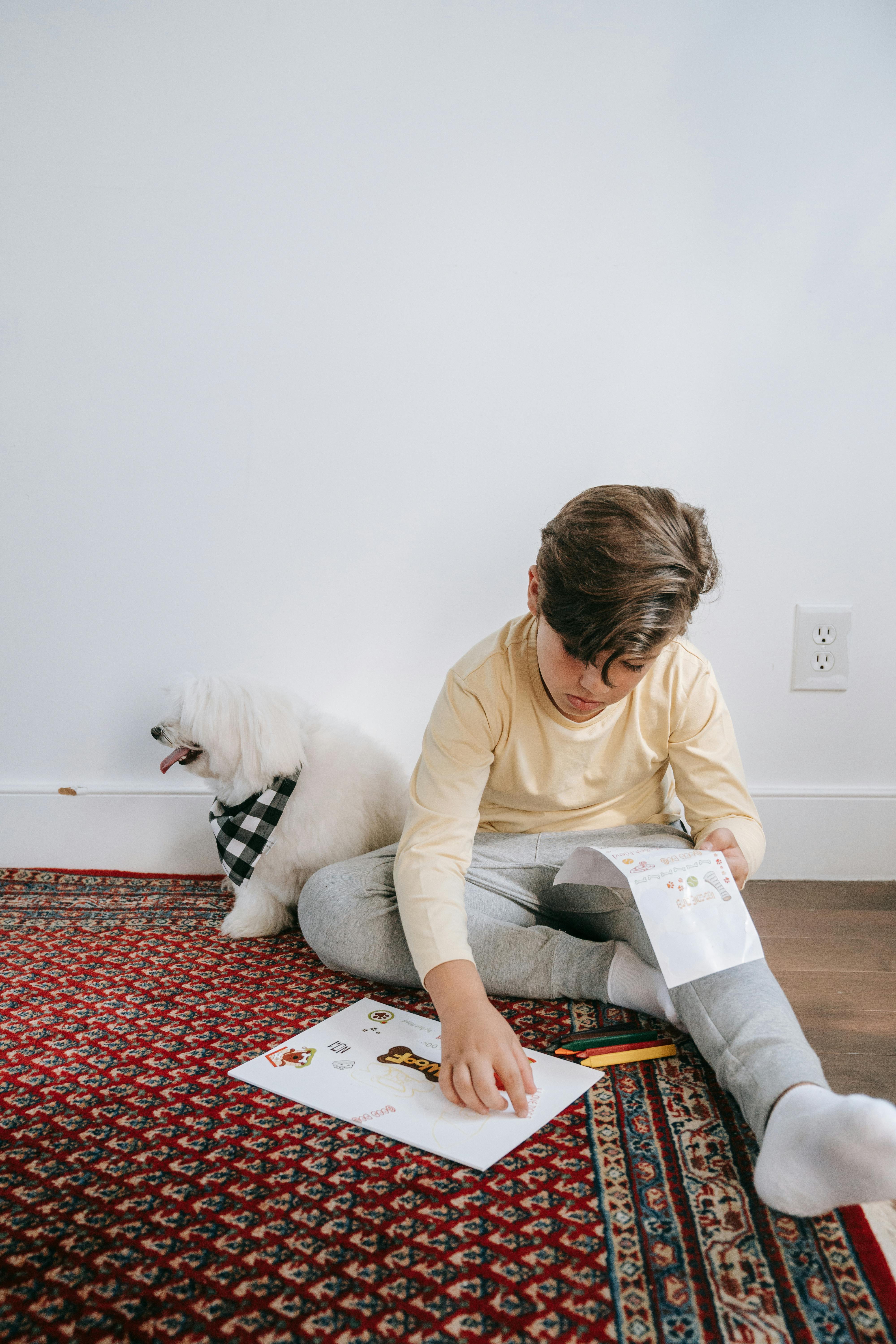 A Kid Putting Stickers on a Paper Near His Dog · Free Stock Photo