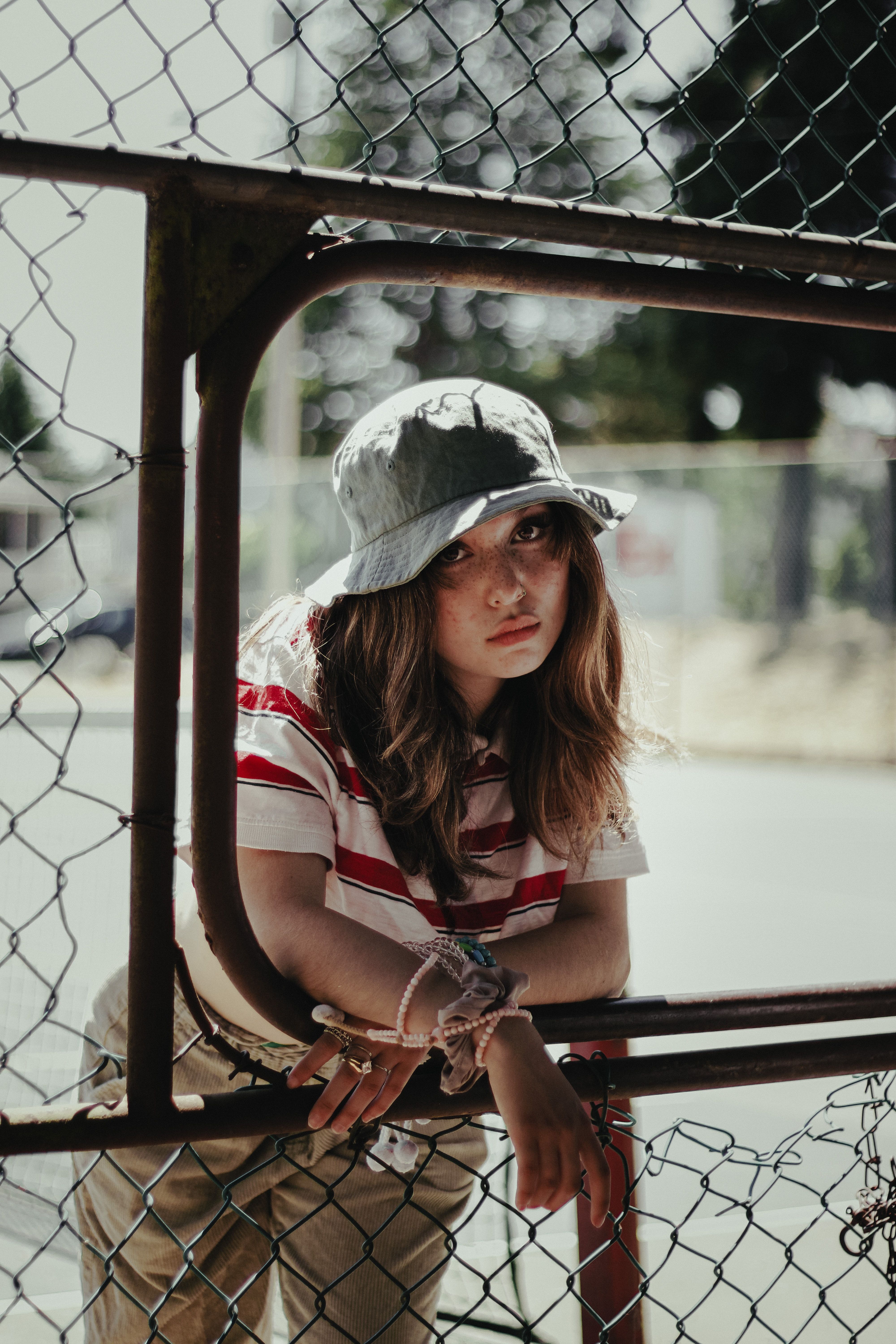 Photo of a Girl in a Bucket Hat Posing on a Chain Fence · Free Stock Photo