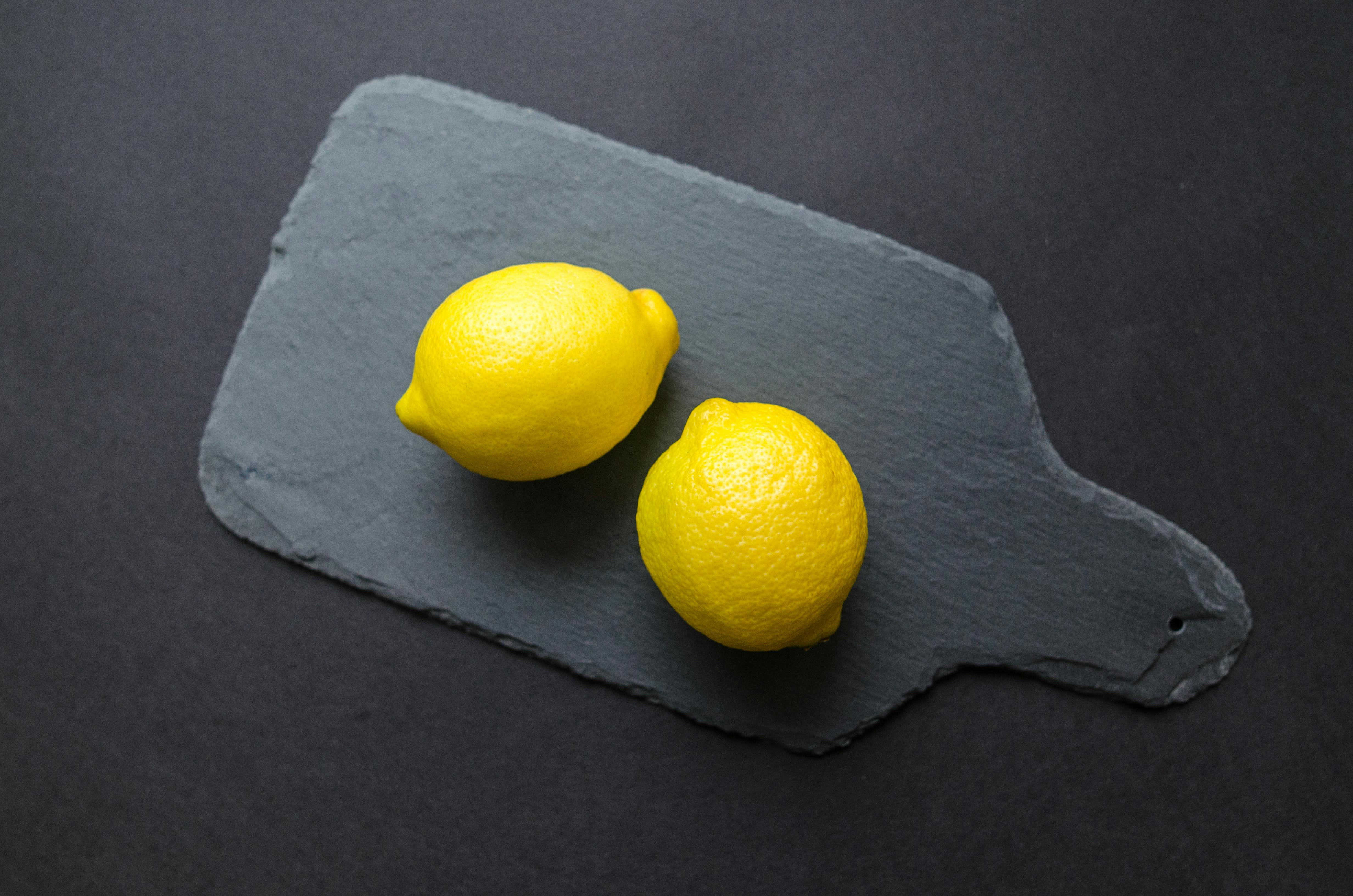 Two Lemons on Black Wooden Pad · Free Stock Photo