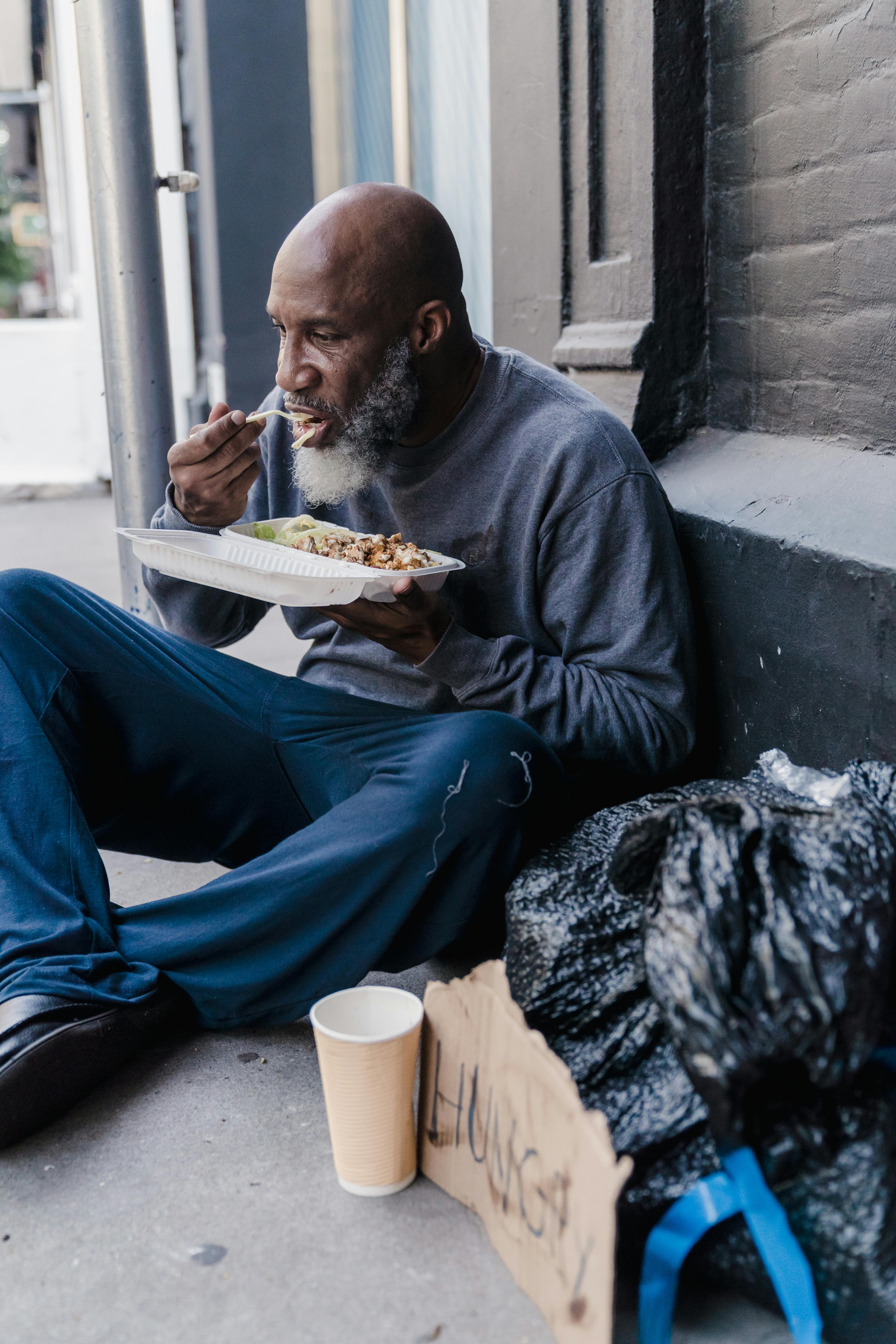 Homeless Man Eating While Sitting on Floor · Free Stock Photo