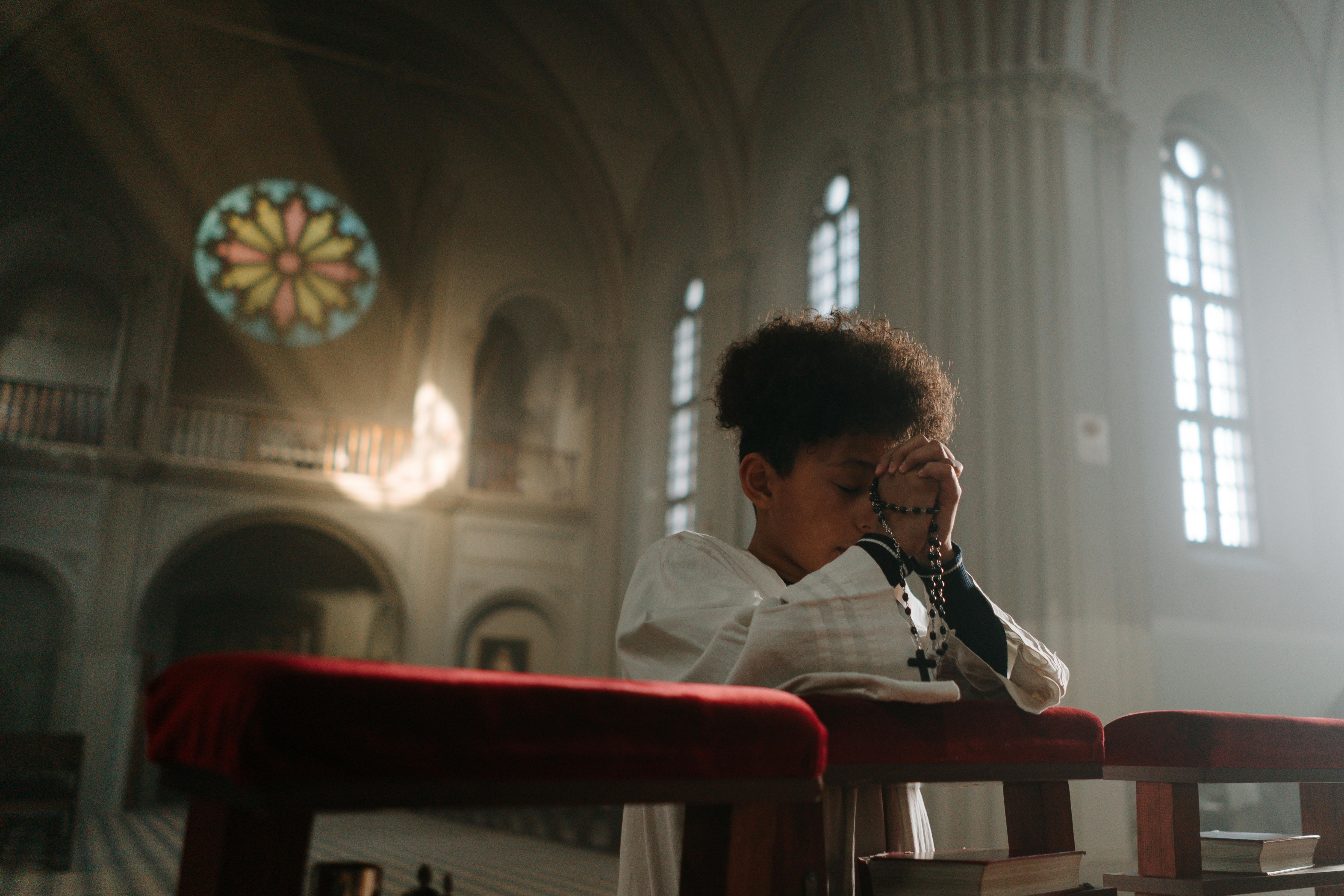 A Boy Praying and Kneeling Inside a Church · Free Stock Photo