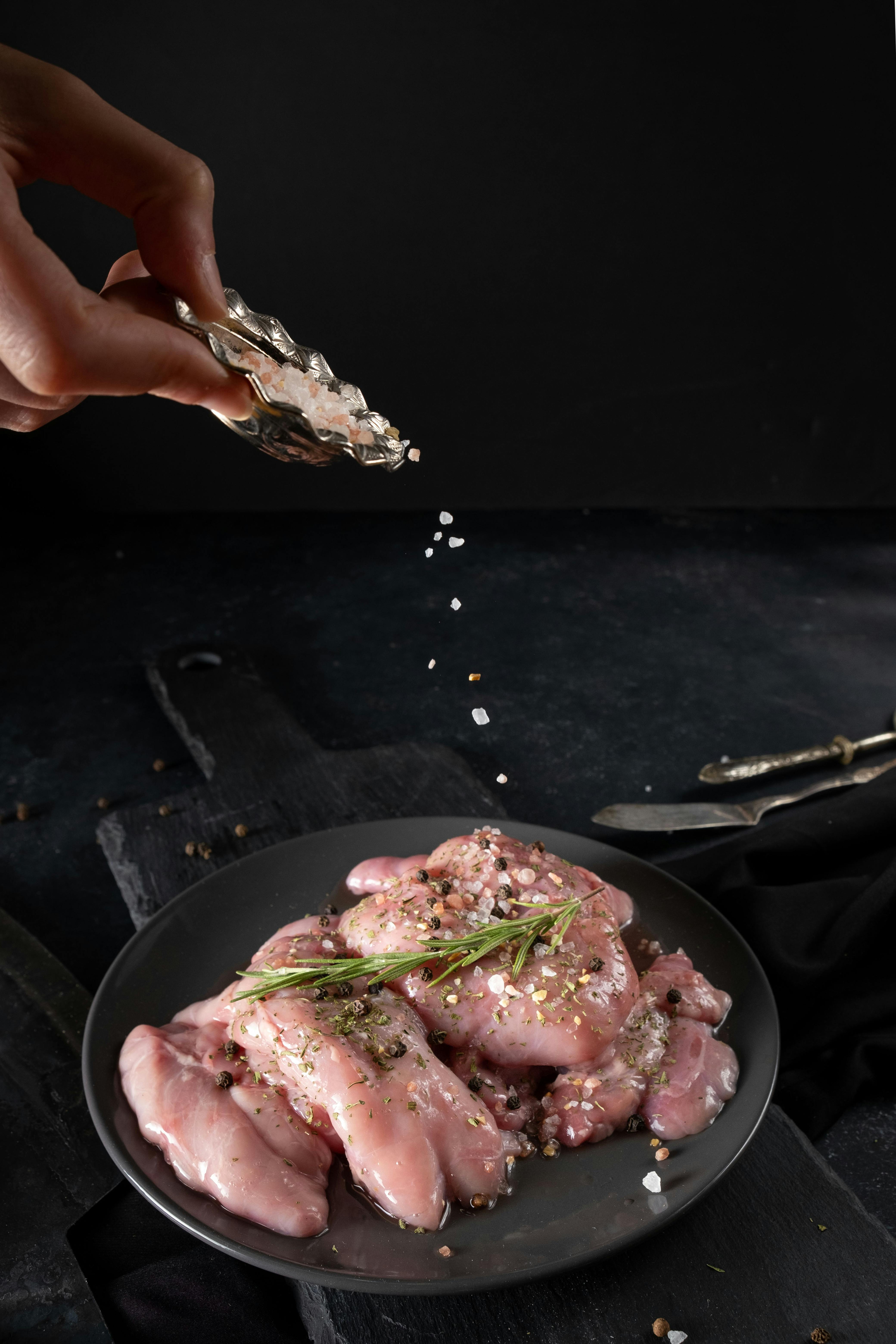Photo of a Person Pouring Salt on Raw Chicken · Free Stock Photo